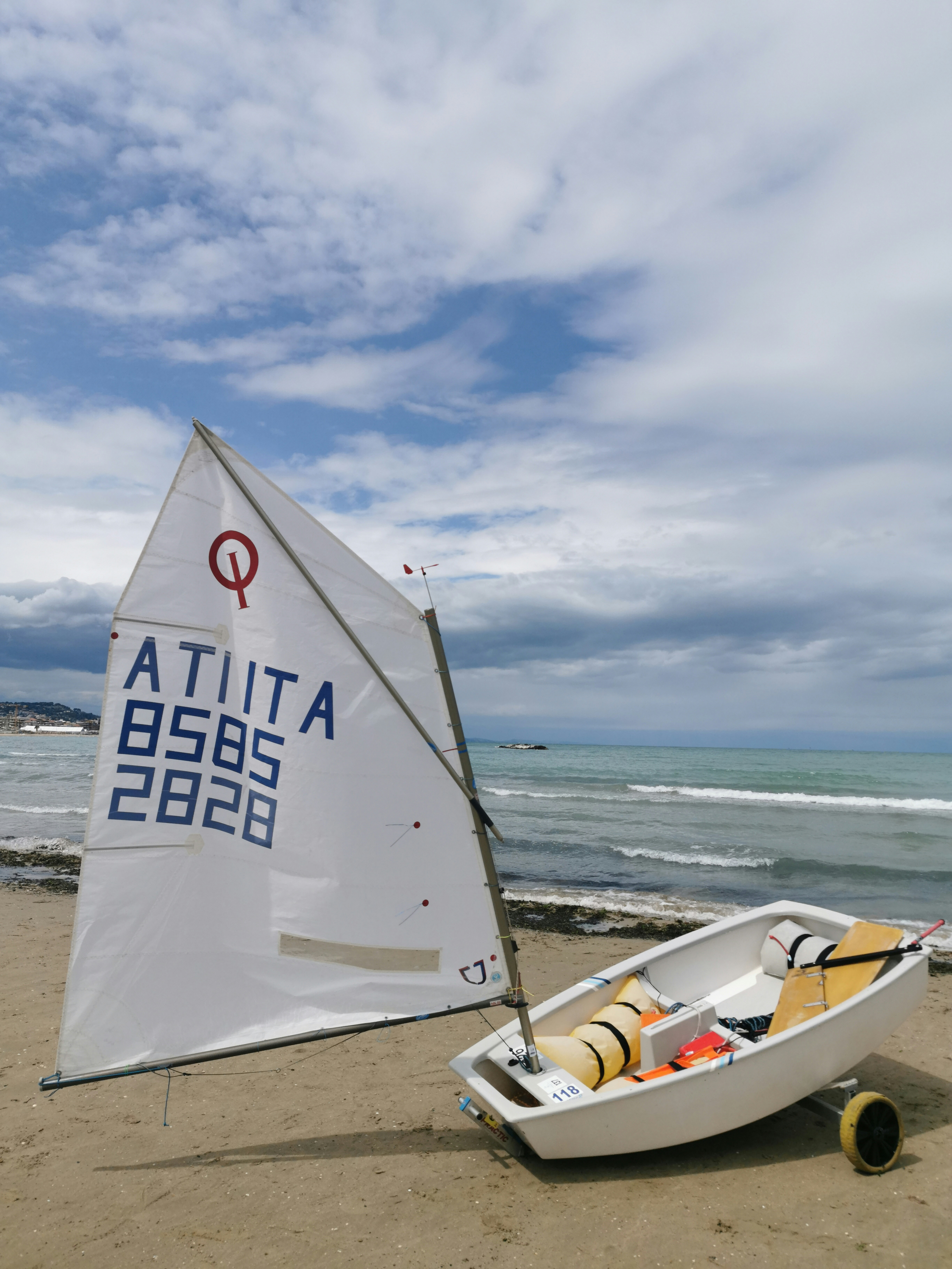 Small sailboat with a single sail rests on a sandy beach under a partly cloudy sky.
