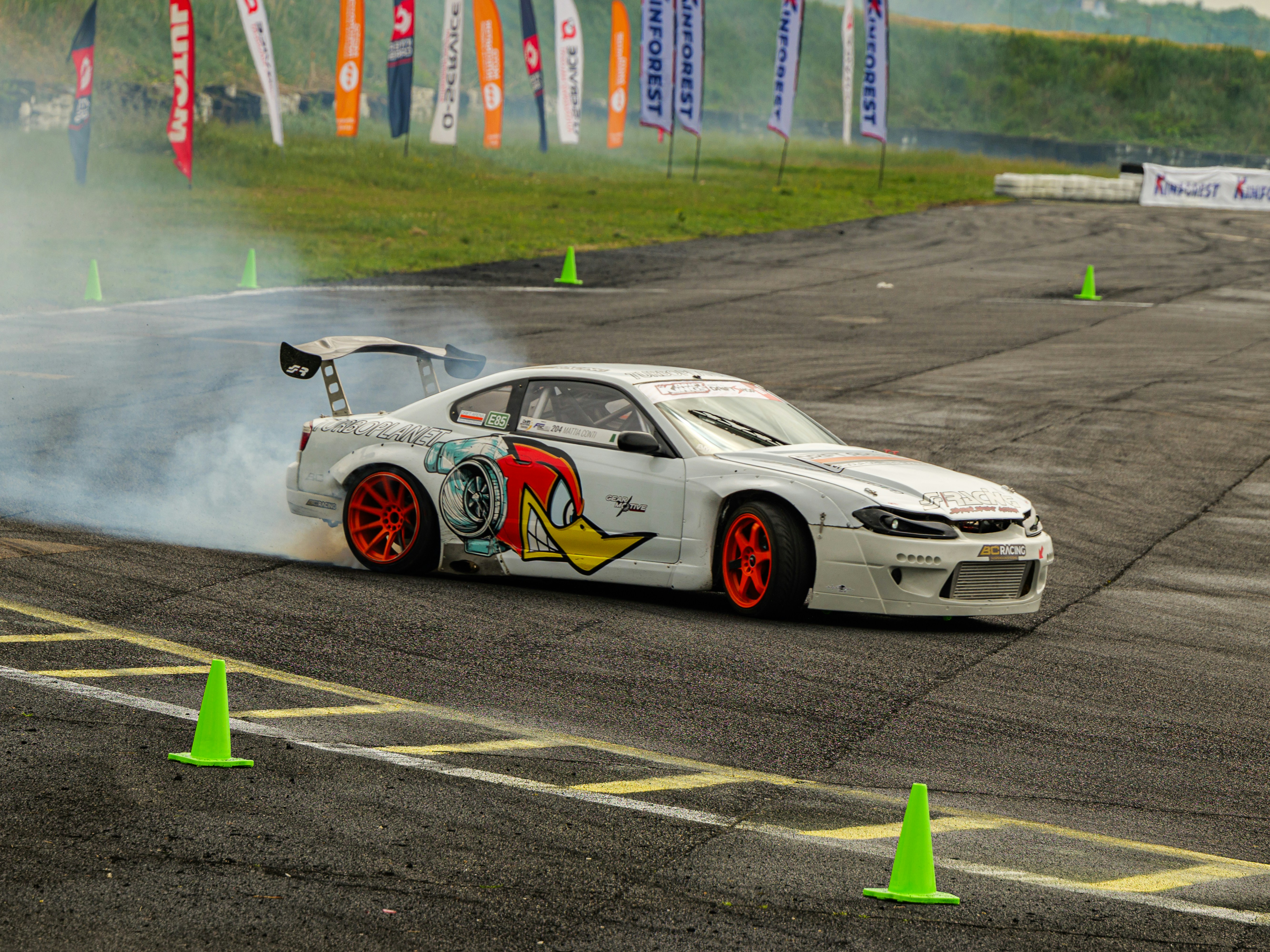 A white car with red rims on a race track with smoke coming out of ...
