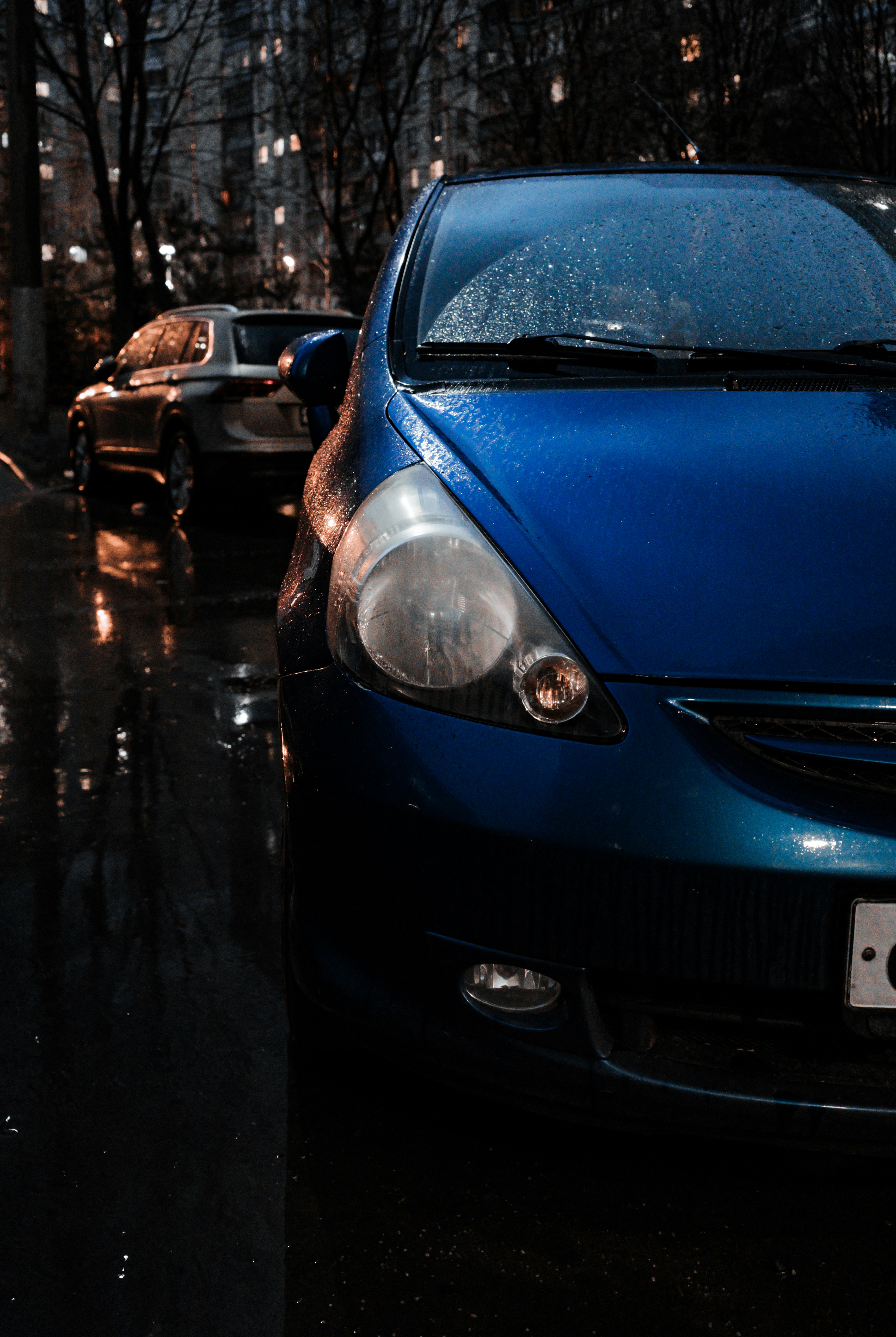 Blue hatchback in rain: a moody street portrait with glistening reflections