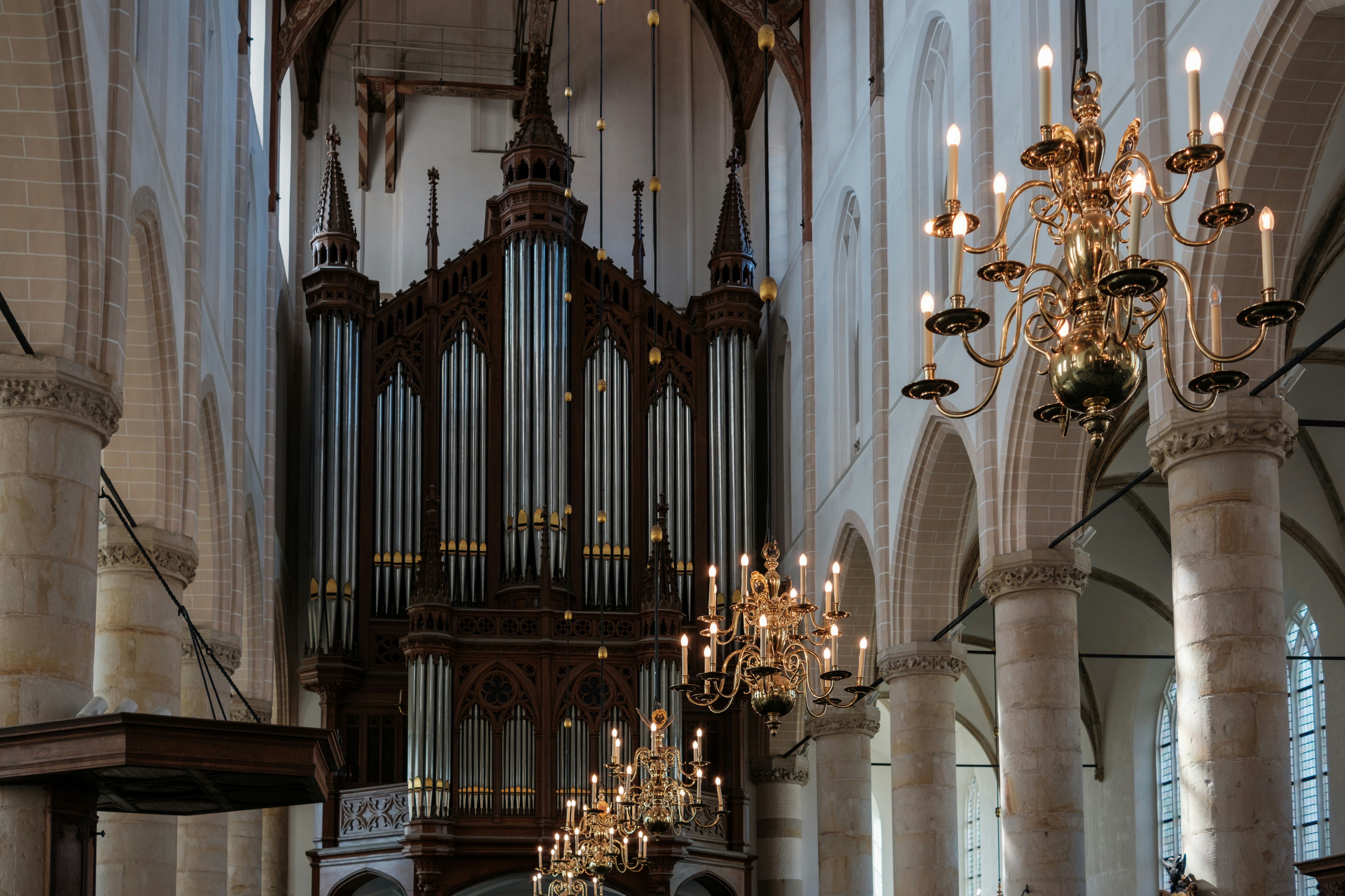 Ornate church organ flanked by elegant chandeliers within a grand gothic cathedral.