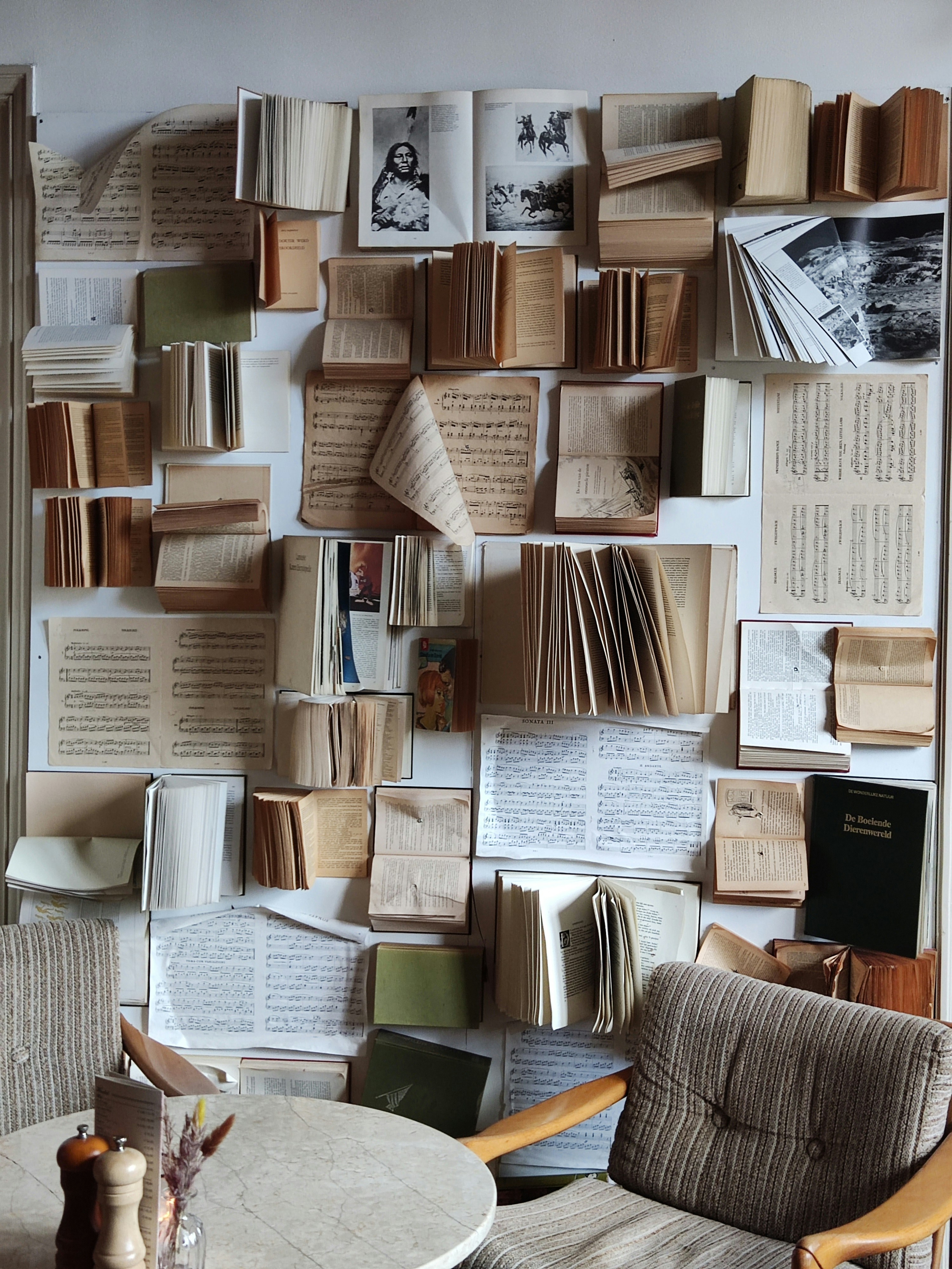 Books and pages artfully arranged on a wall above a cozy chair and round table.