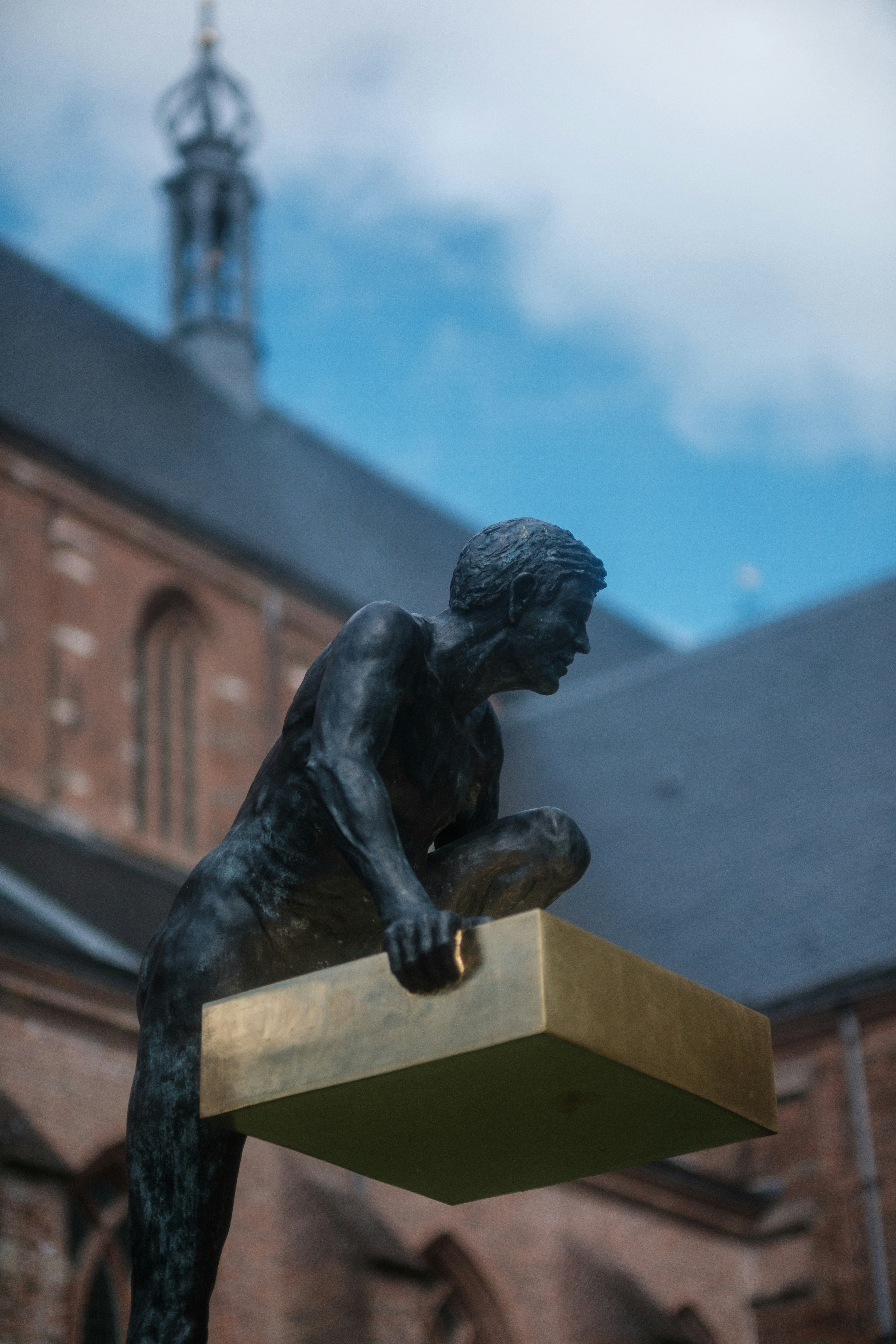 Bronze Figure Over a Brass Plinth, Framed by a Red-Brick Church Under a Clear Blue Sky