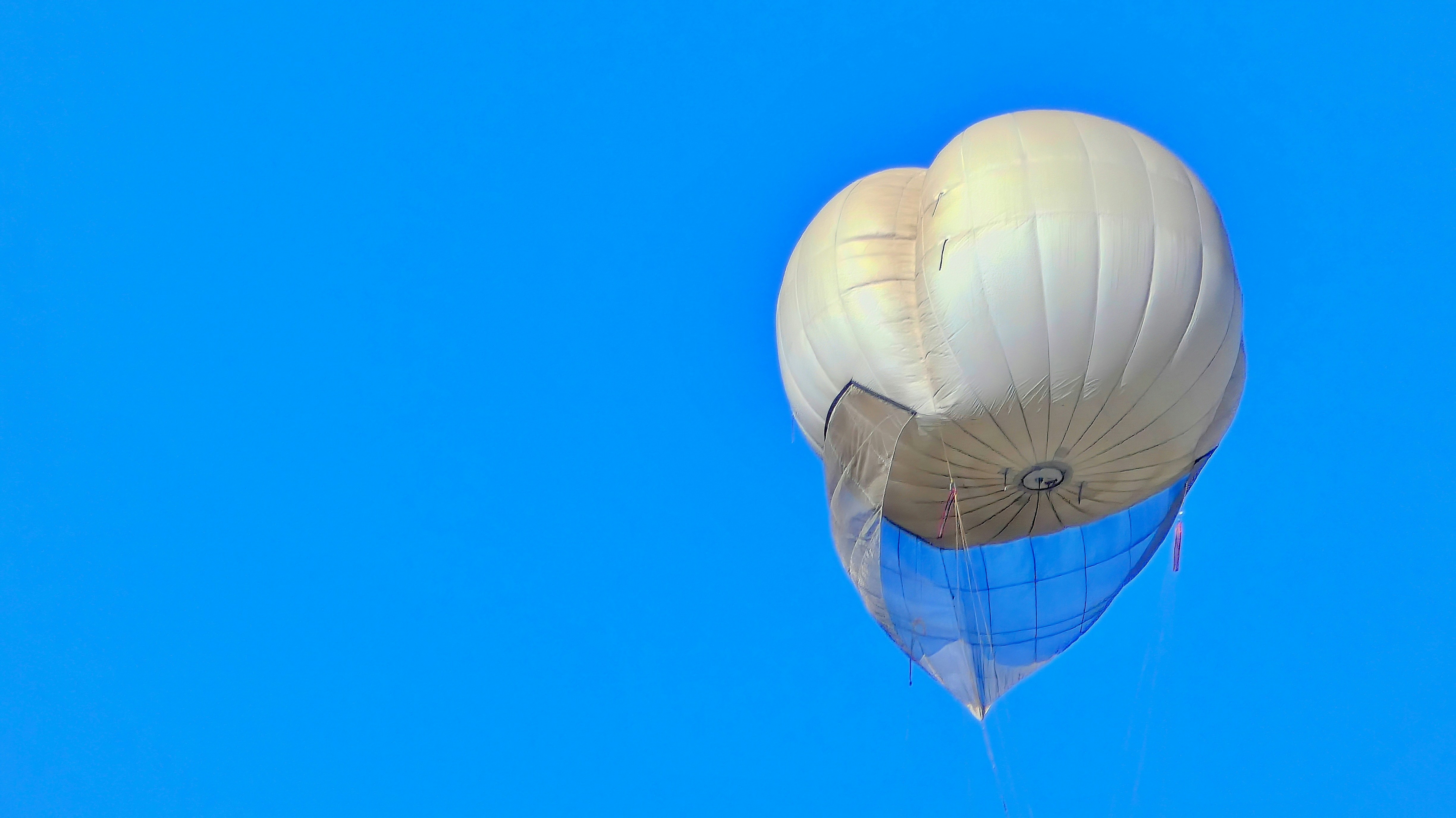 Cream parachute with blue canopy against a vivid blue sky, suspended on thin cords; minimal landscape, focusing on the floating capsule-like canopy.