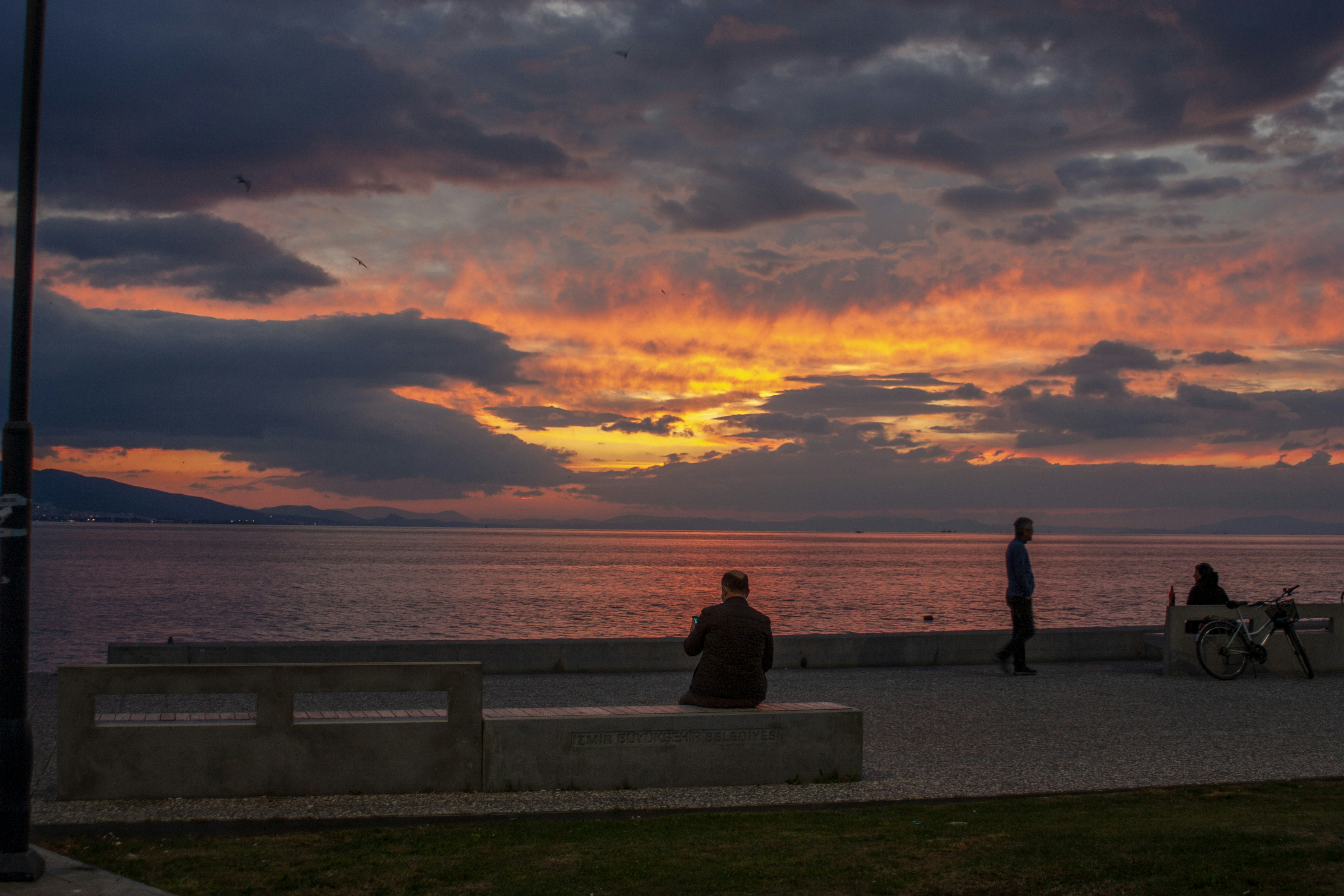 Silhouetted figures sit on a seaside bench against a vibrant sunset sky.