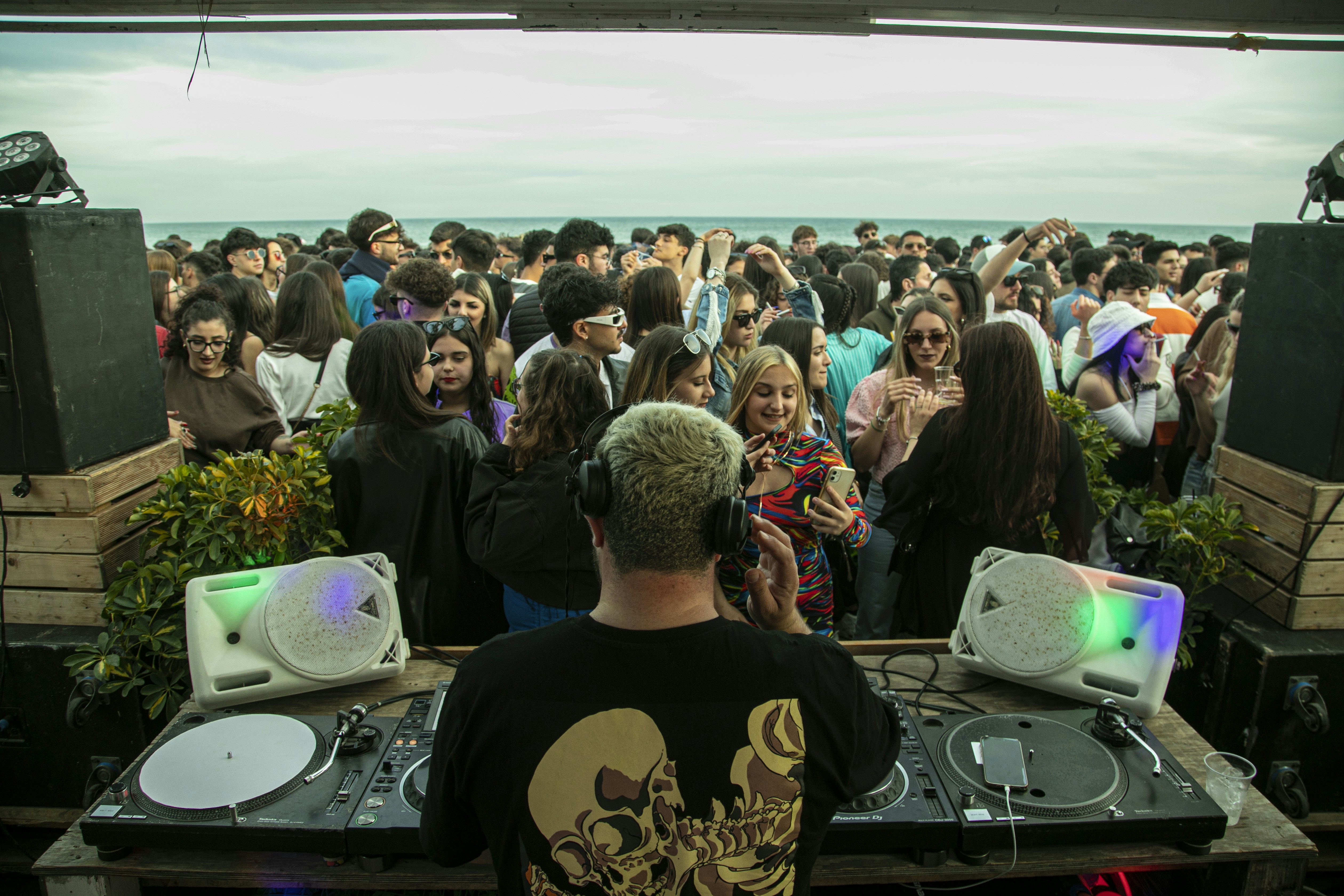Deckside Pulse: A Rooftop DJ Orchestrates a Sea of Faces by the Ocean