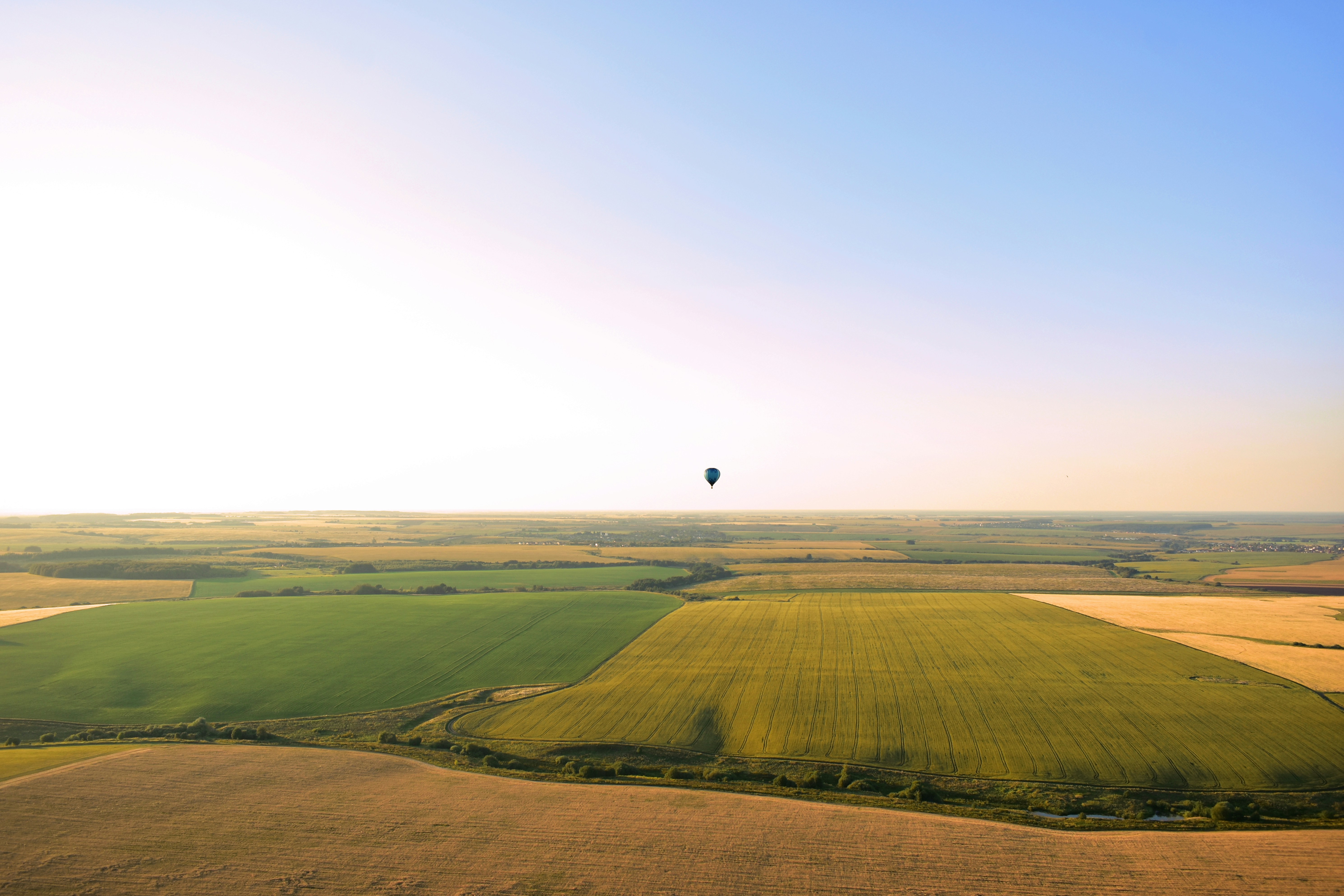 A lone hot-air balloon drifts above rolling fields at golden hour