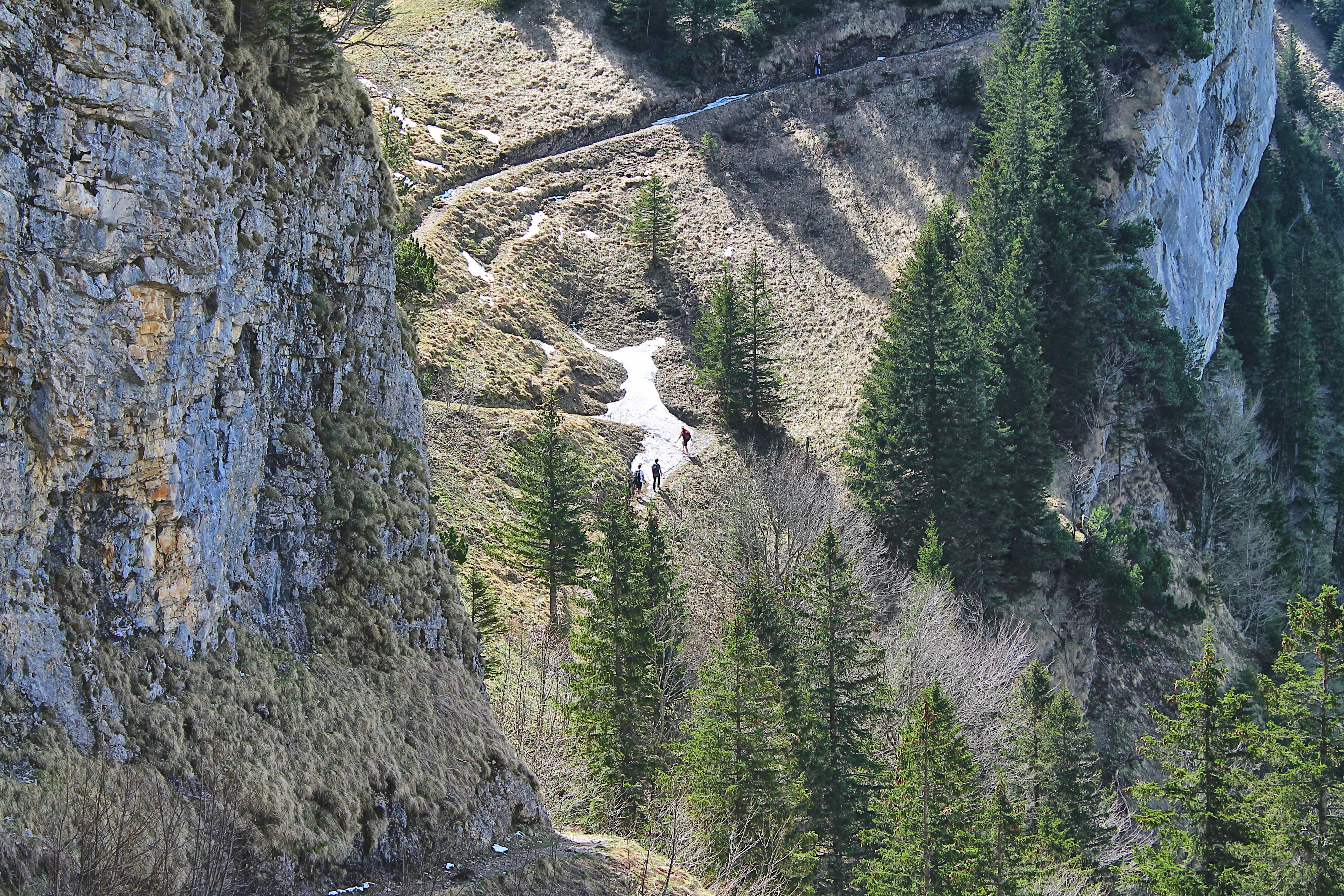 Narrow Alpine Corridor: Hikers Trek a Snow-dusted Gorge Between Granite Cliffs