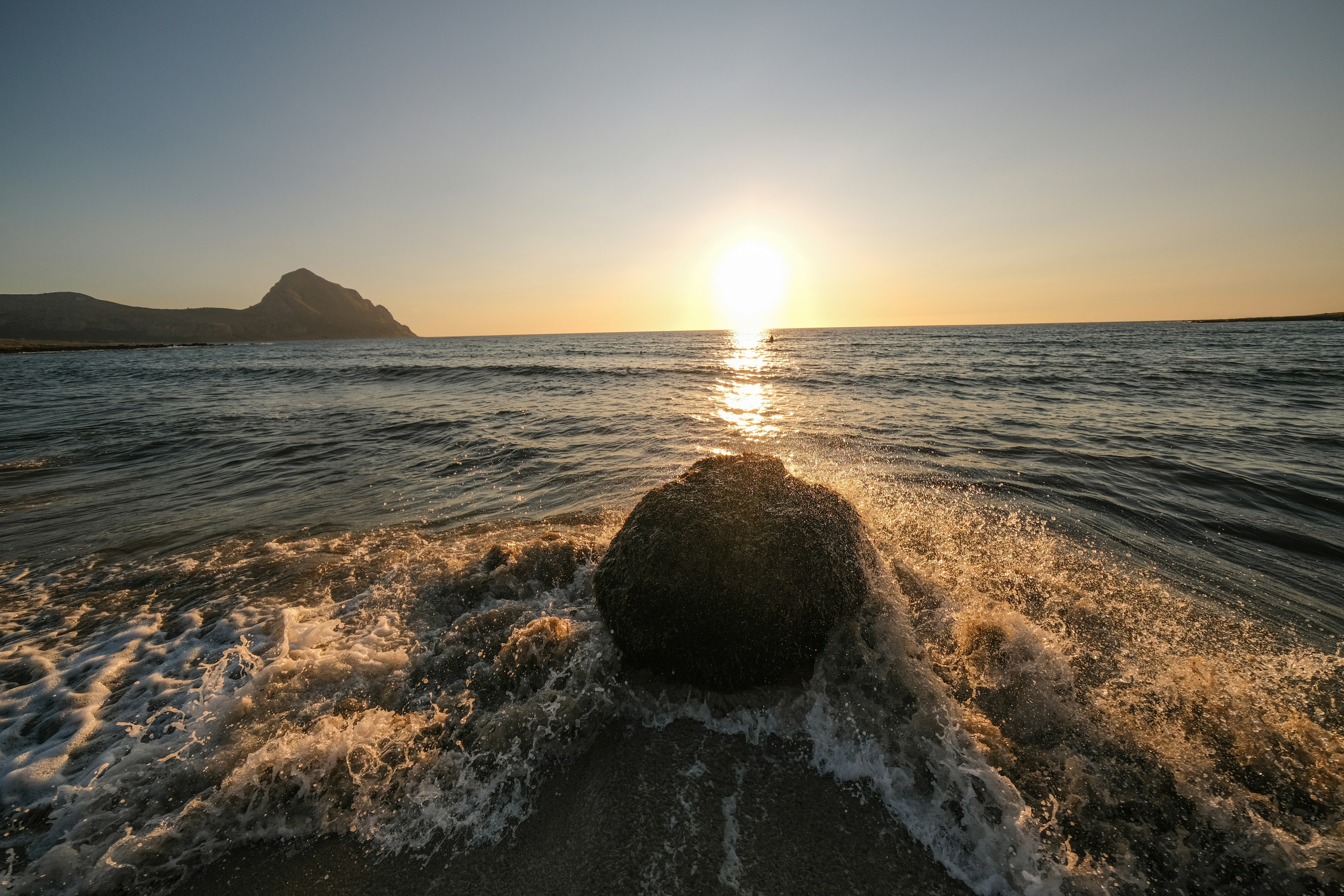 El sol se está poniendo sobre el océano con una roca que sobresale del ...