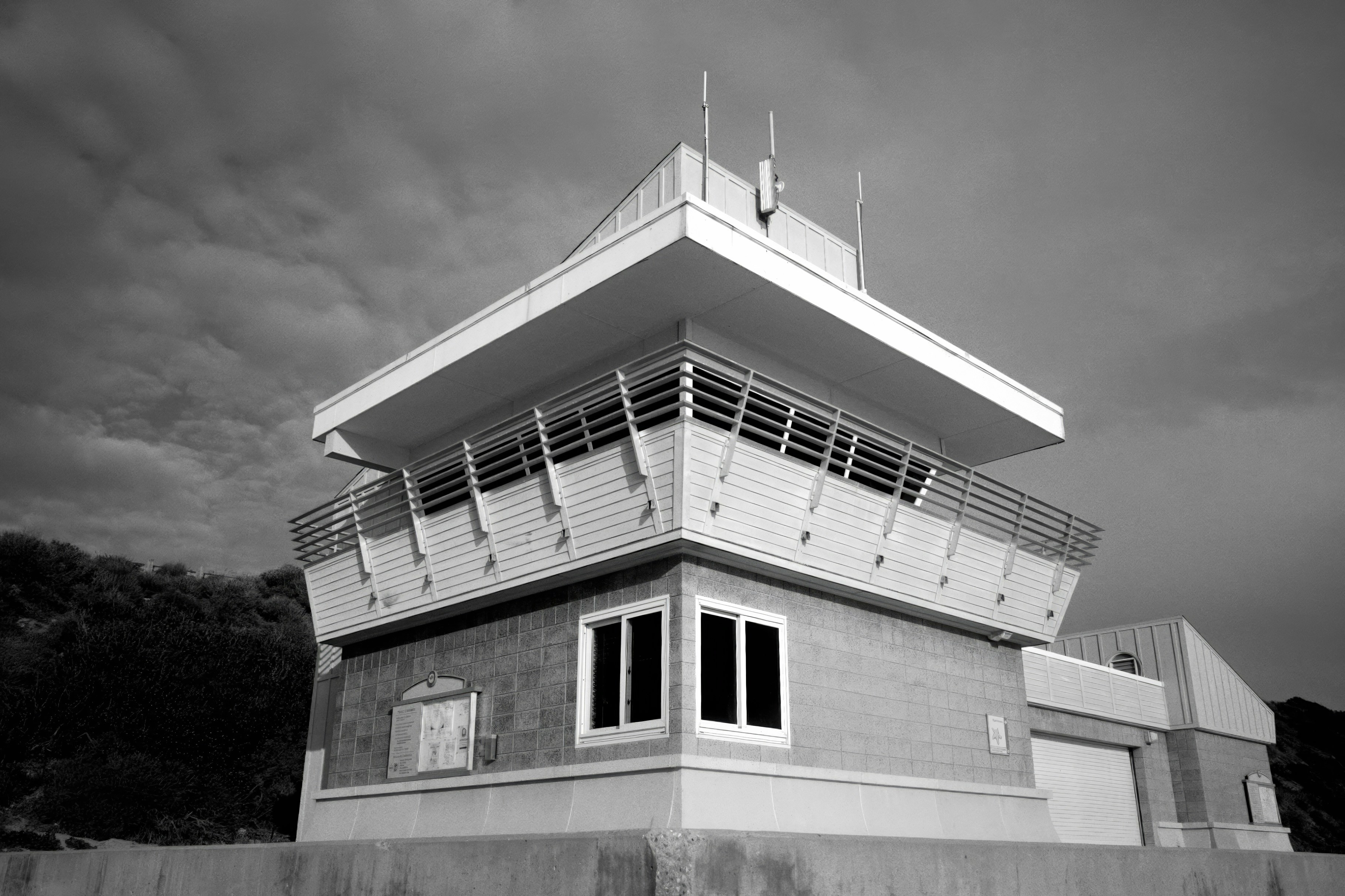 Modern lifeguard tower with angular architecture against a dramatic sky in black and white.