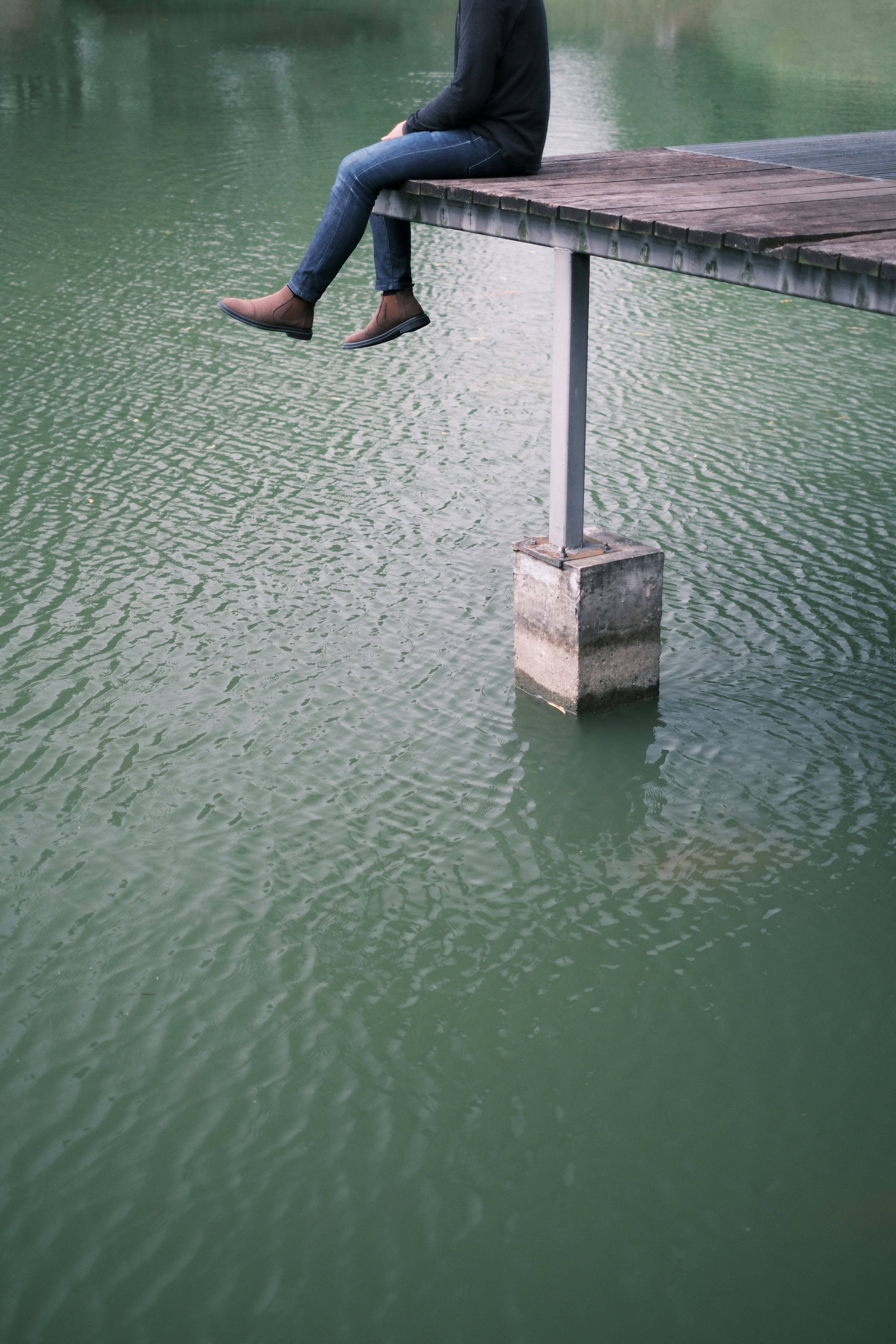 Edge of Stillness: Boots Dangling Over Green Water