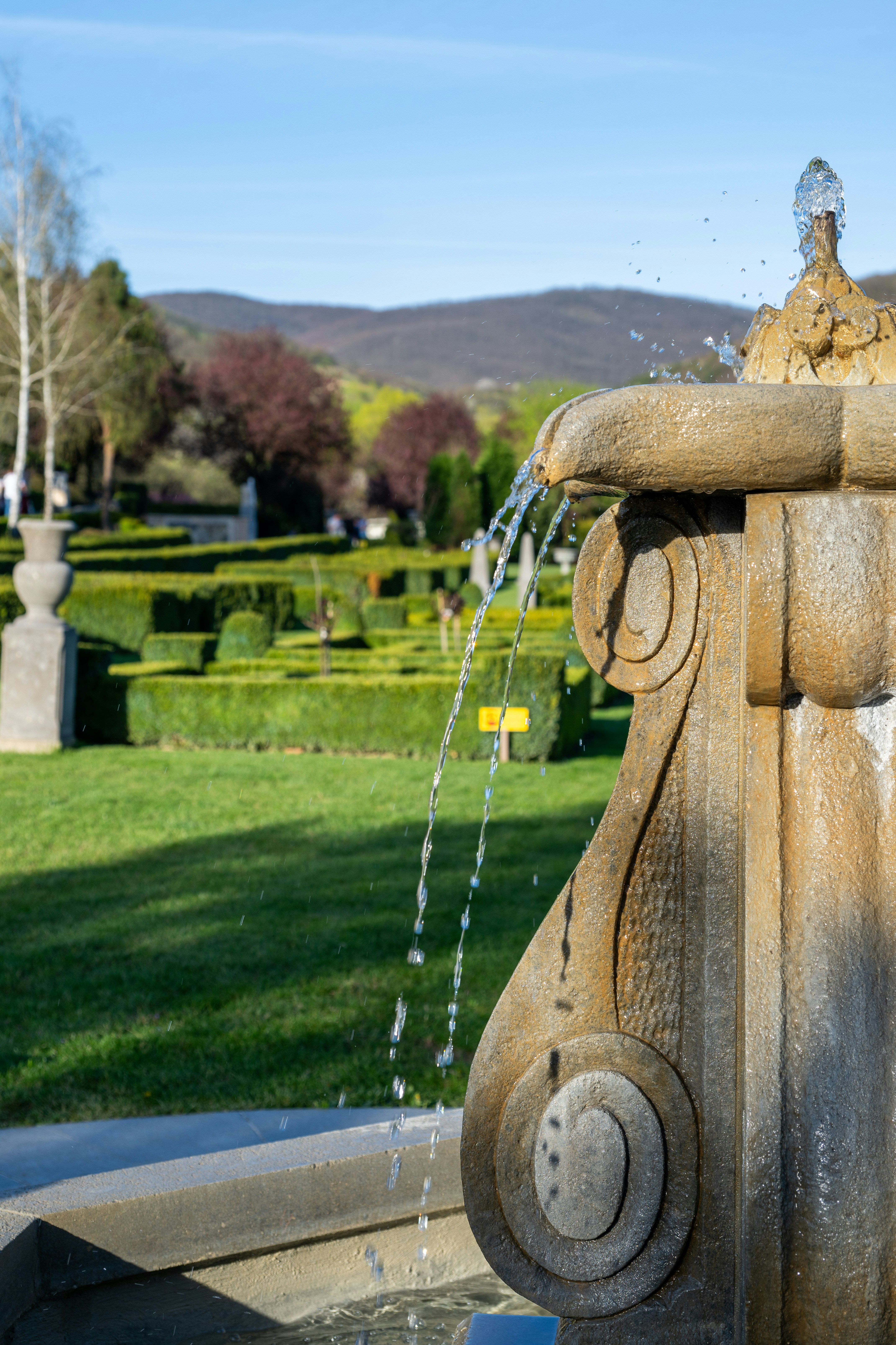 Sunlit Stone Fountain Framed by Pruned Hedges and Distant Hills