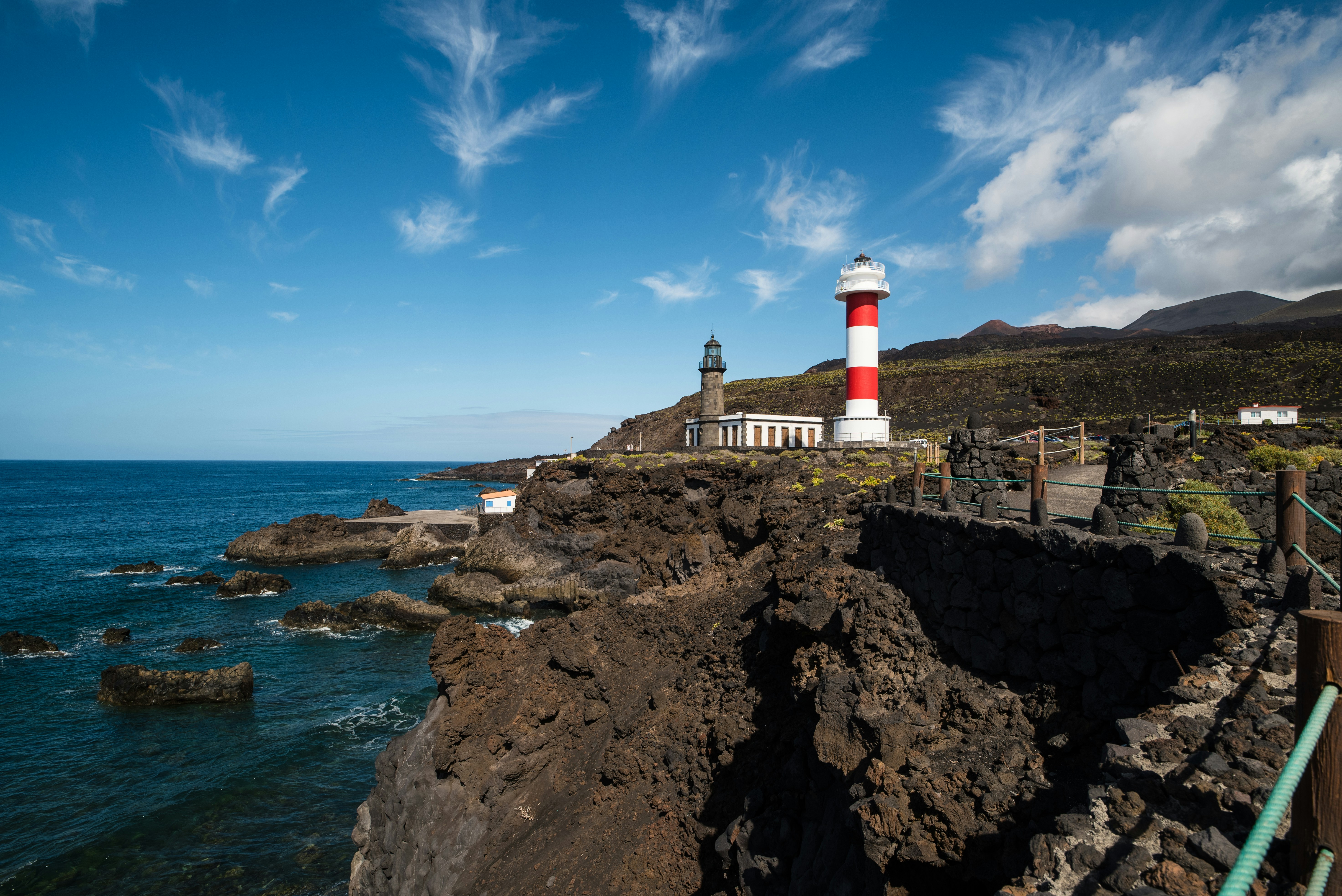 Lighthouse on volcanic coast: red-and-white beacon overlooking rugged lava rocks
