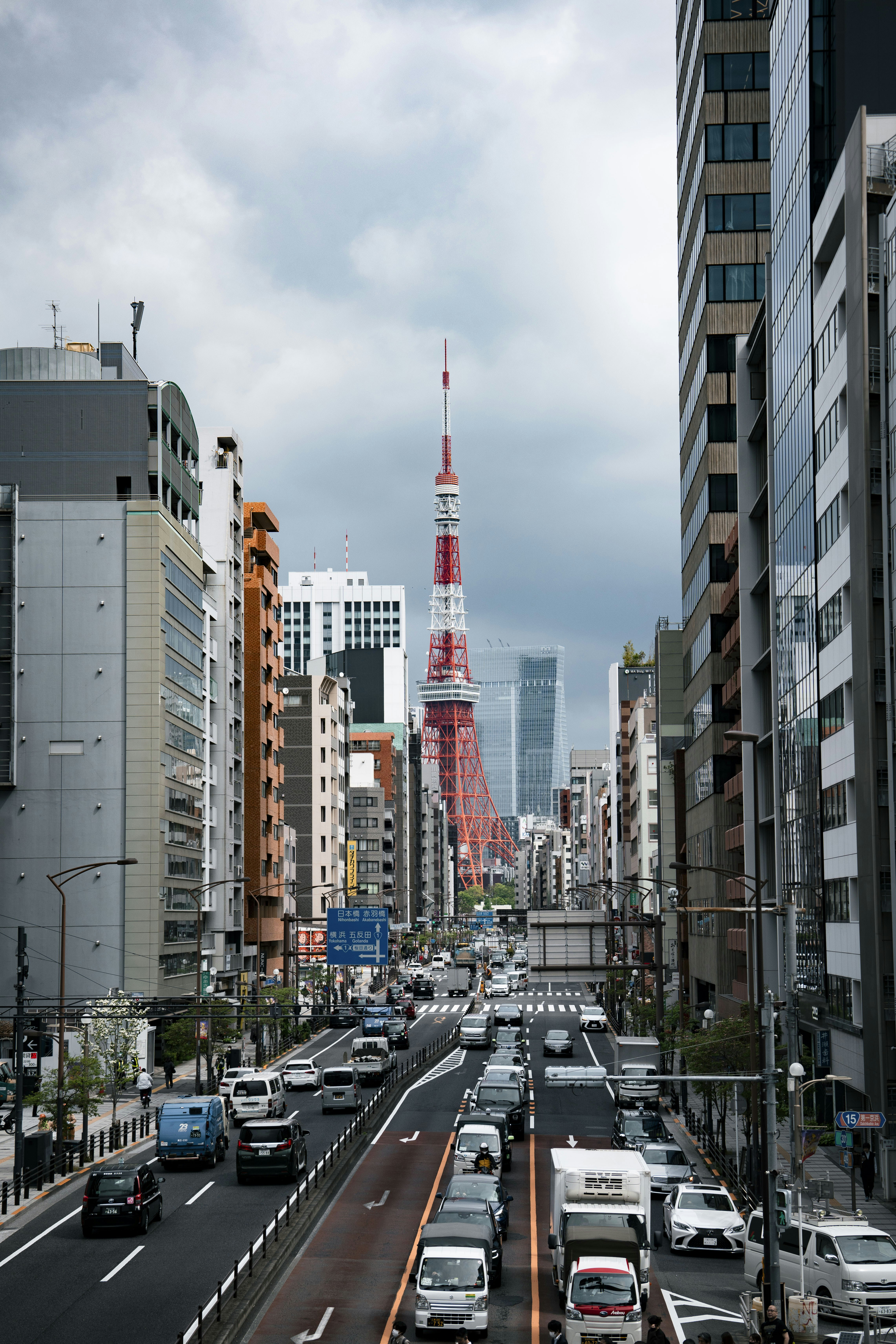 Tokyo Tower rises prominently among modern skyscrapers, framed by bustling city streets filled with vehicles. A blend of tradition and urban life unfolds.