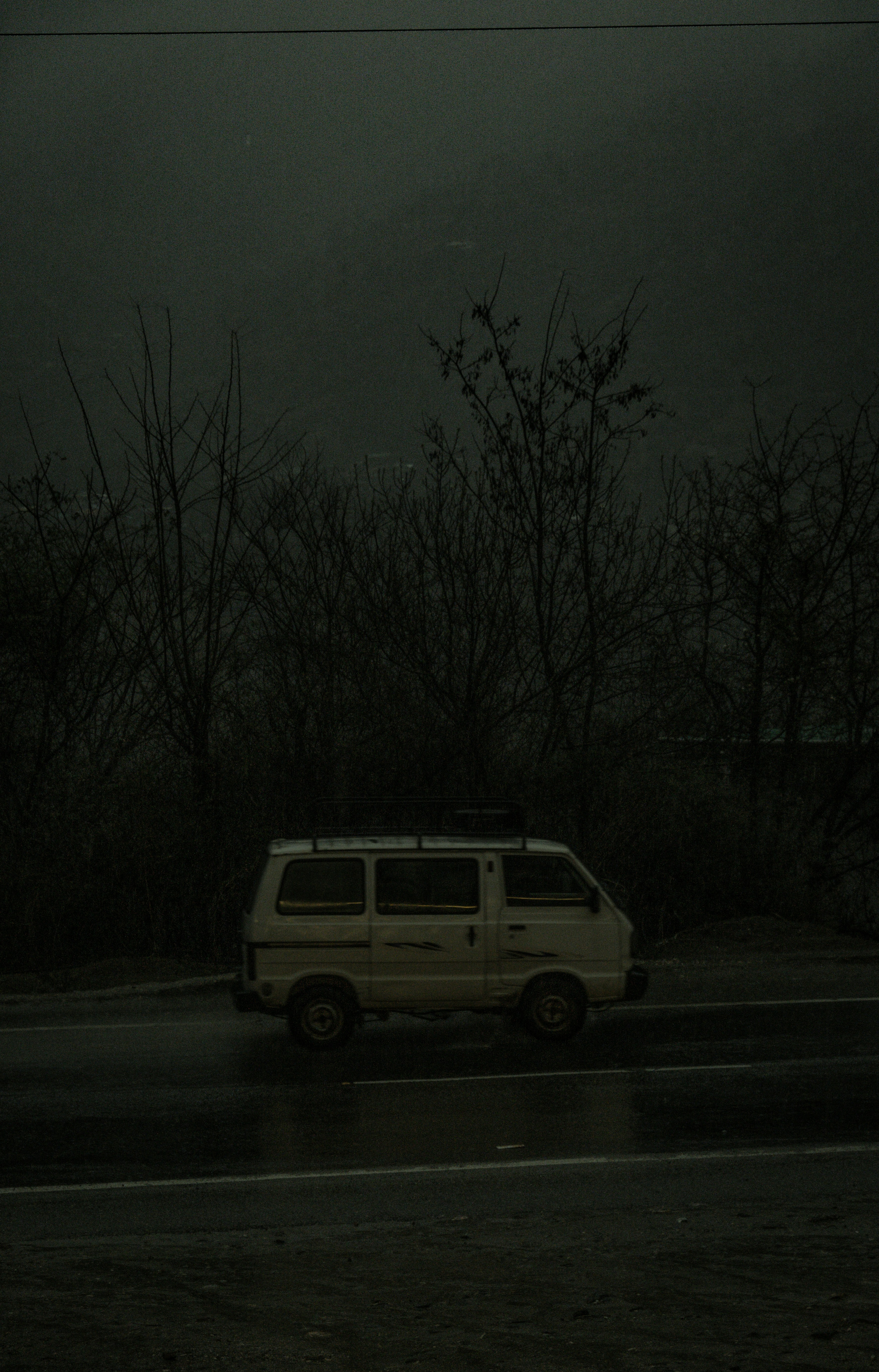 Midnight Static: A Weathered Van Resting on a Wet Highway Beneath Skeletal Trees