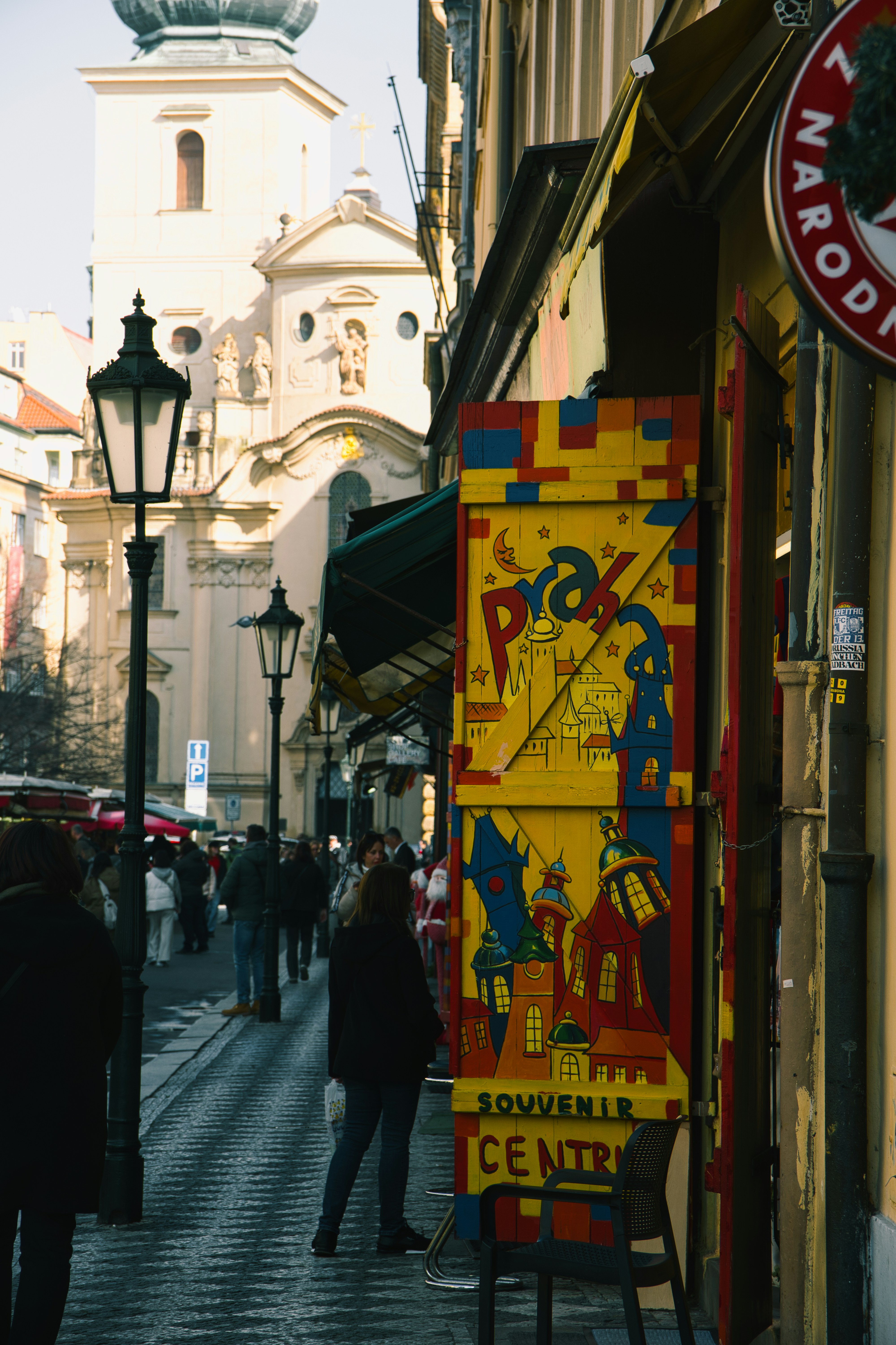 Kaleidoscopic kiosk mural brightens a cobbled European street beside a baroque church