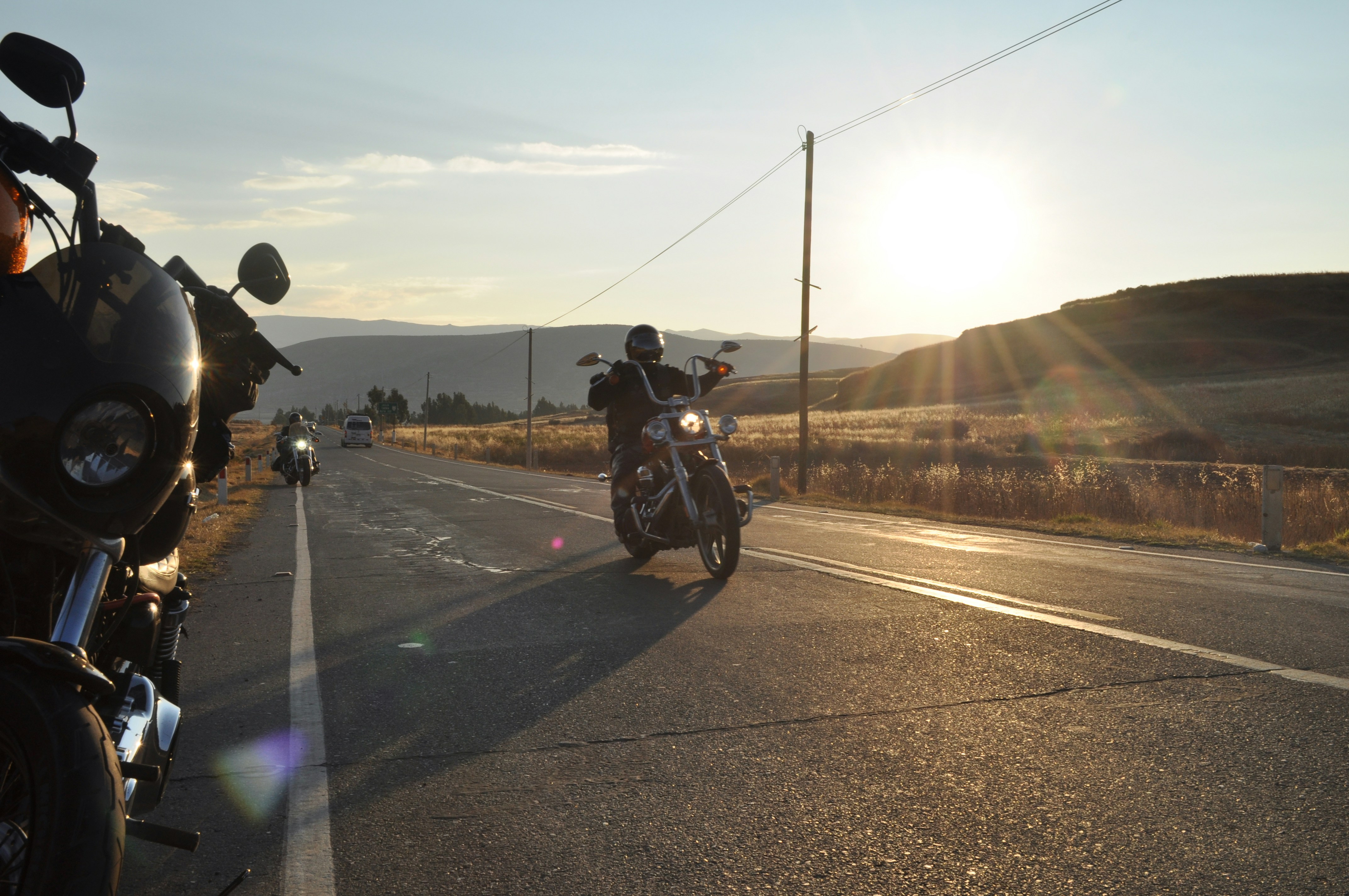 Motorcyclist cruising along a sunlit rural road with hills in the background.