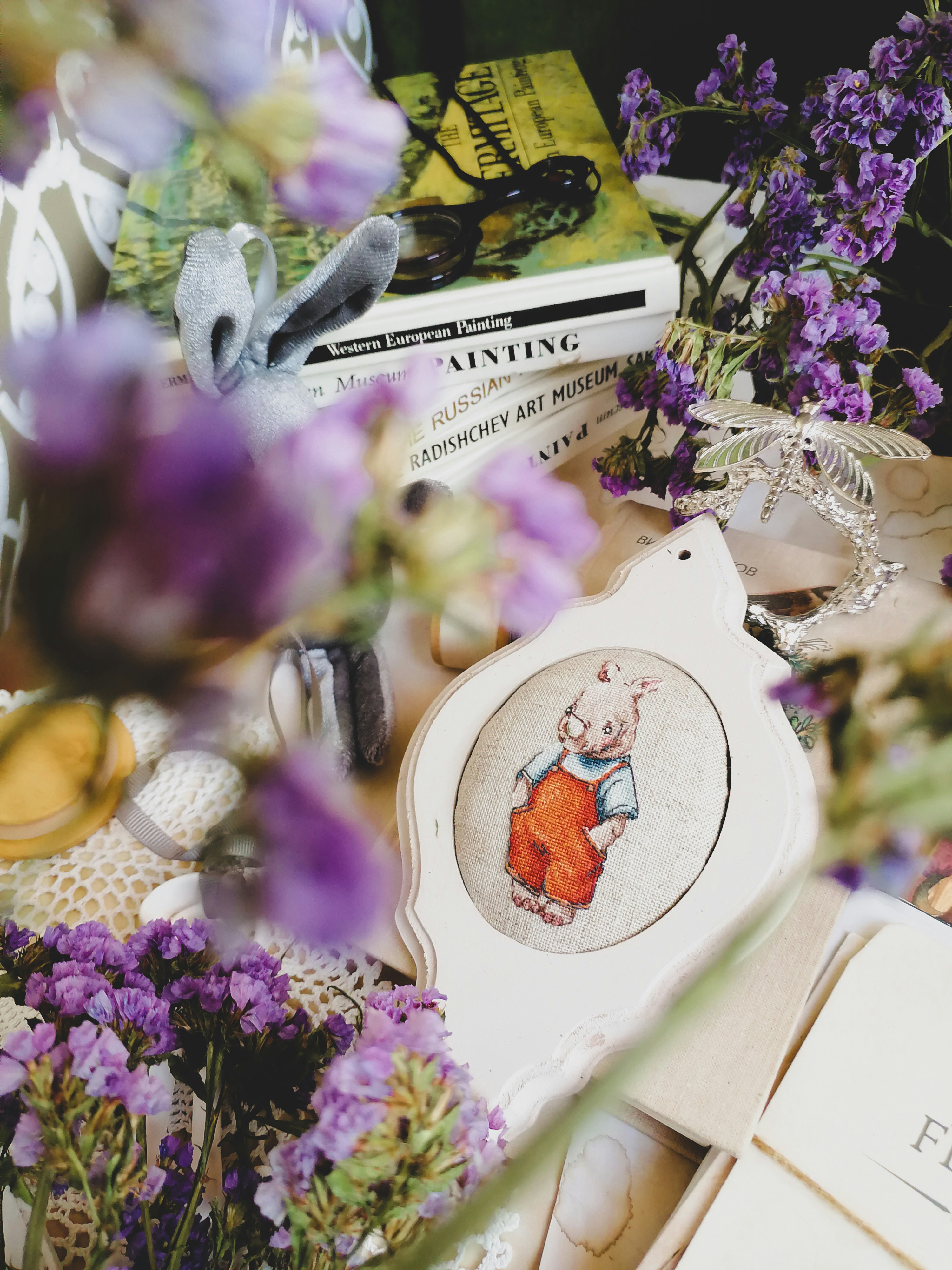 Illustration of a rabbit in red overalls surrounded by lavender flowers and stacked books.