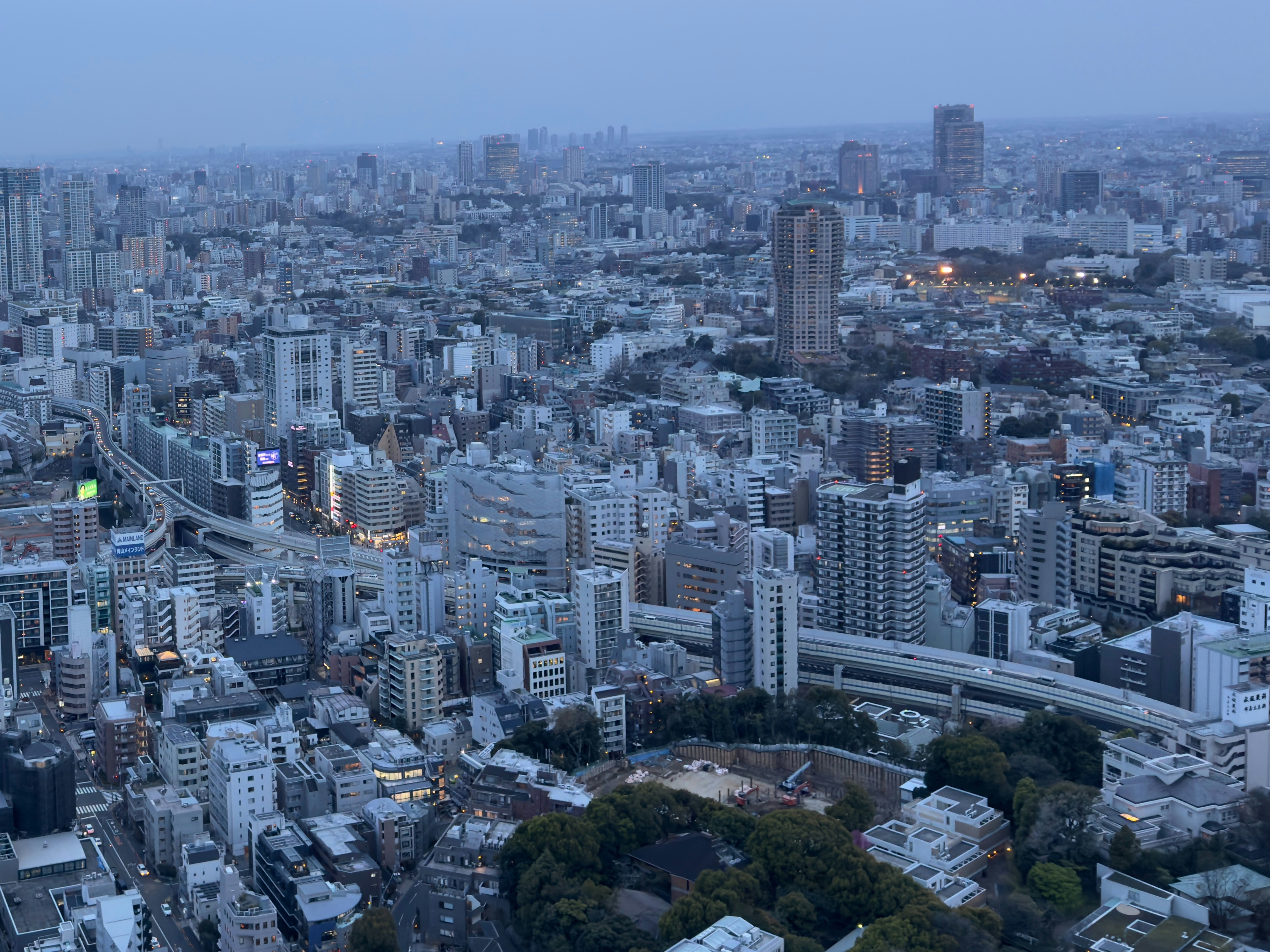 Expansive cityscape with illuminated buildings and winding roads at dusk.