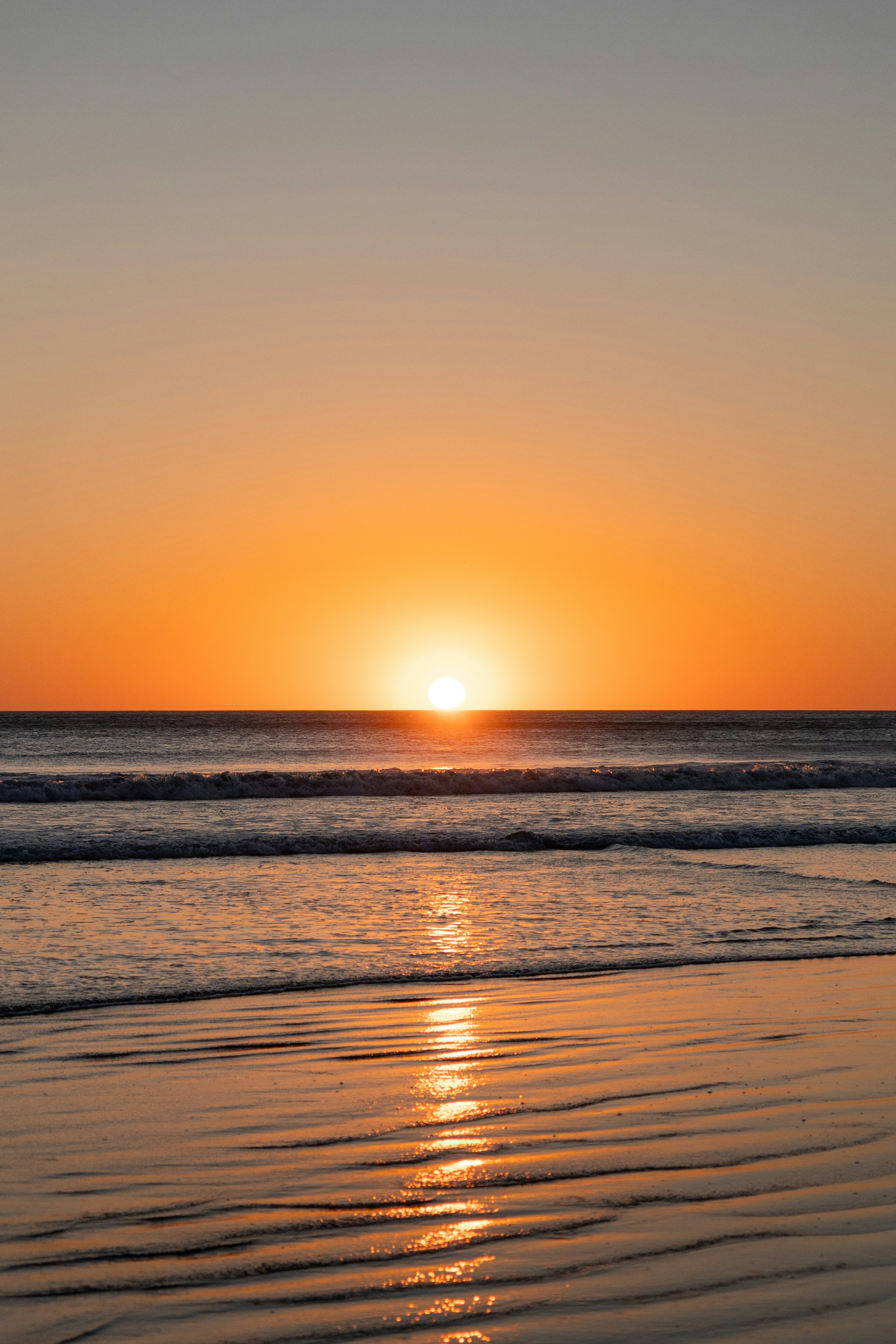Golden sun dipping below the horizon, casting reflections on gentle ocean waves at twilight.