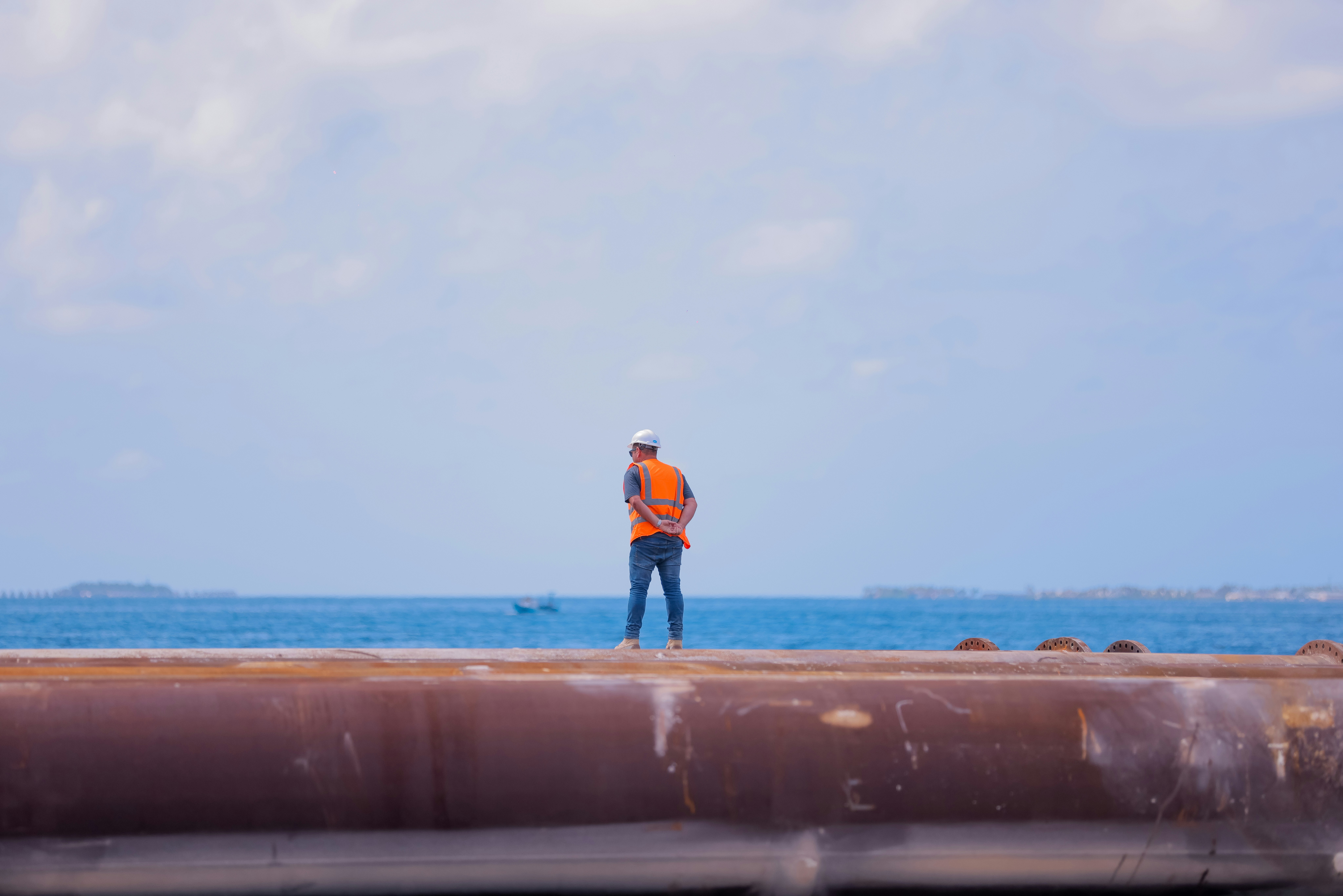 Orange Vest on Rusted Pier: A Lone Worker Against a Minimal Sea