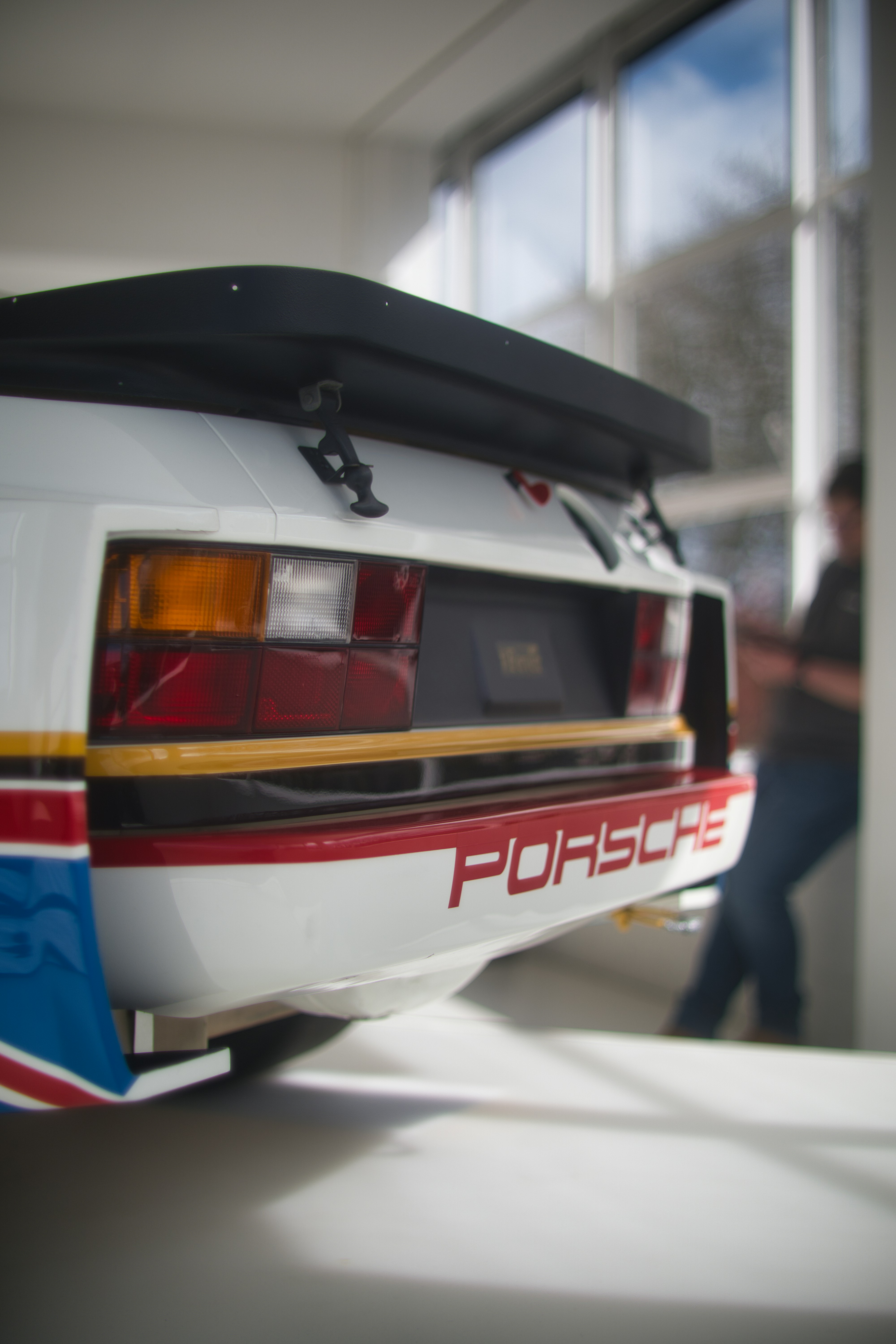 Rear of a Porsche race car on display, with focus on the taillights and livery