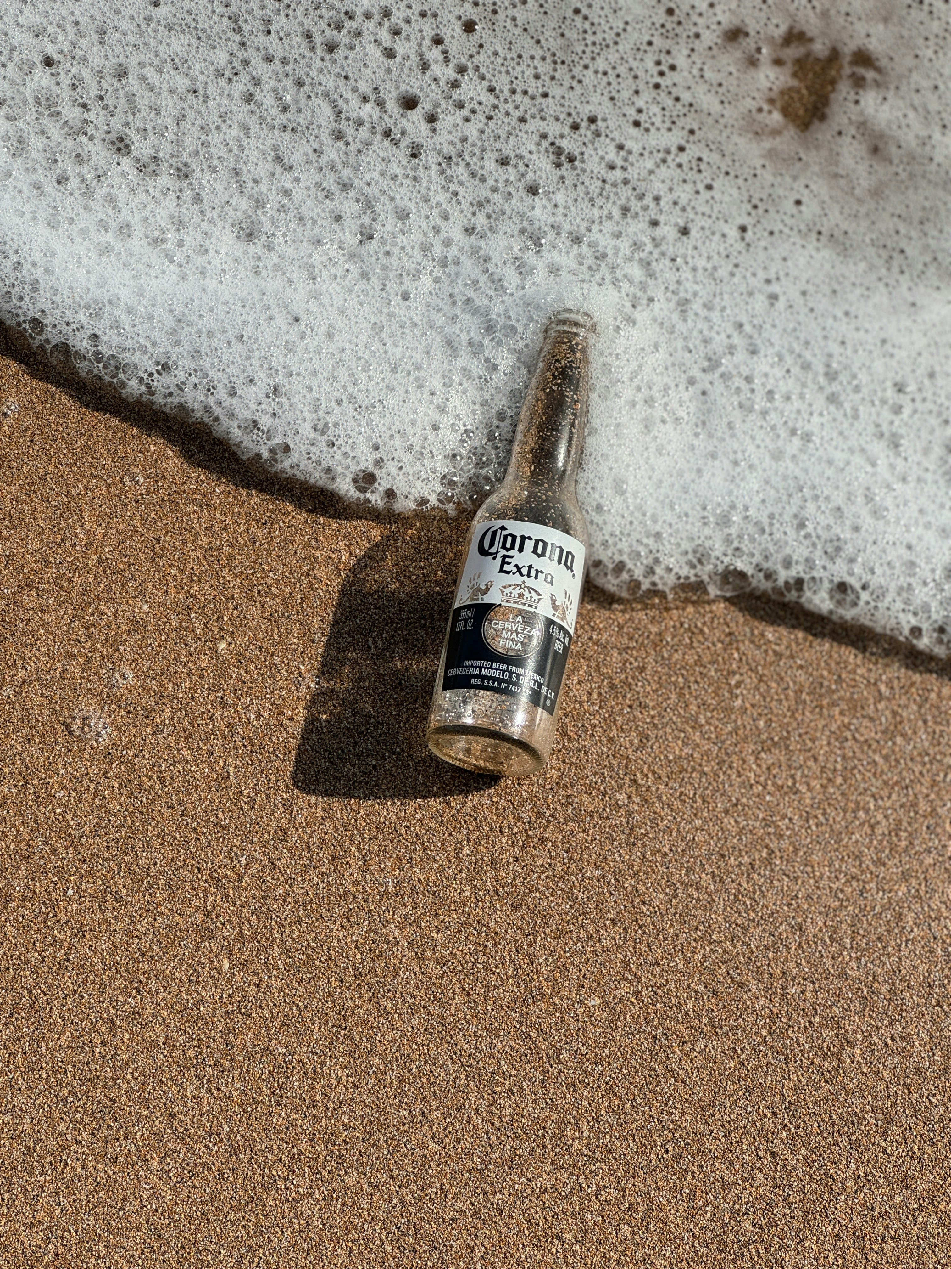 Foamy Edge of the Shore: Corona bottle on sun-warmed sand