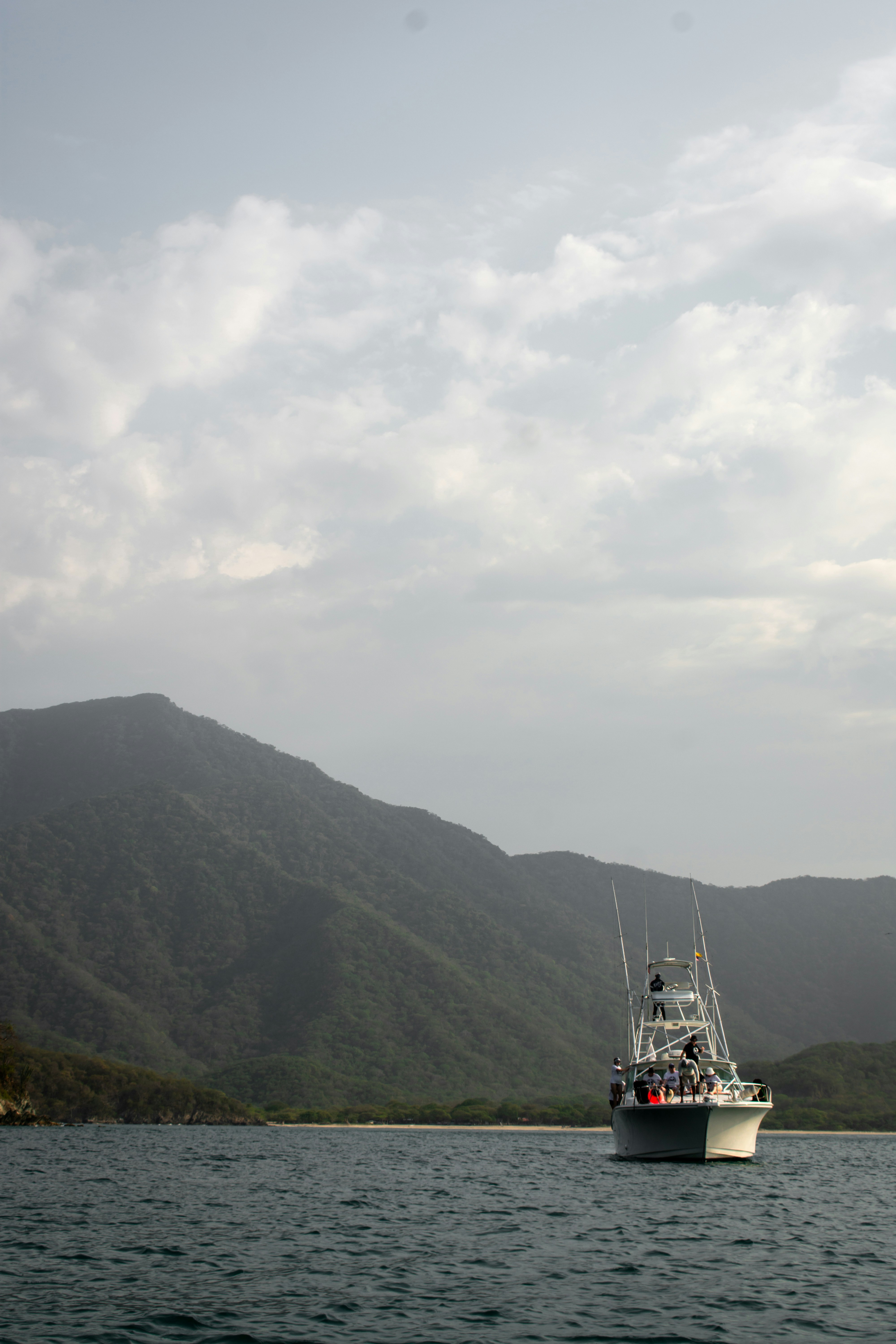 Fishing boat anchored in serene waters with majestic mountains in the background, under a softly clouded sky.