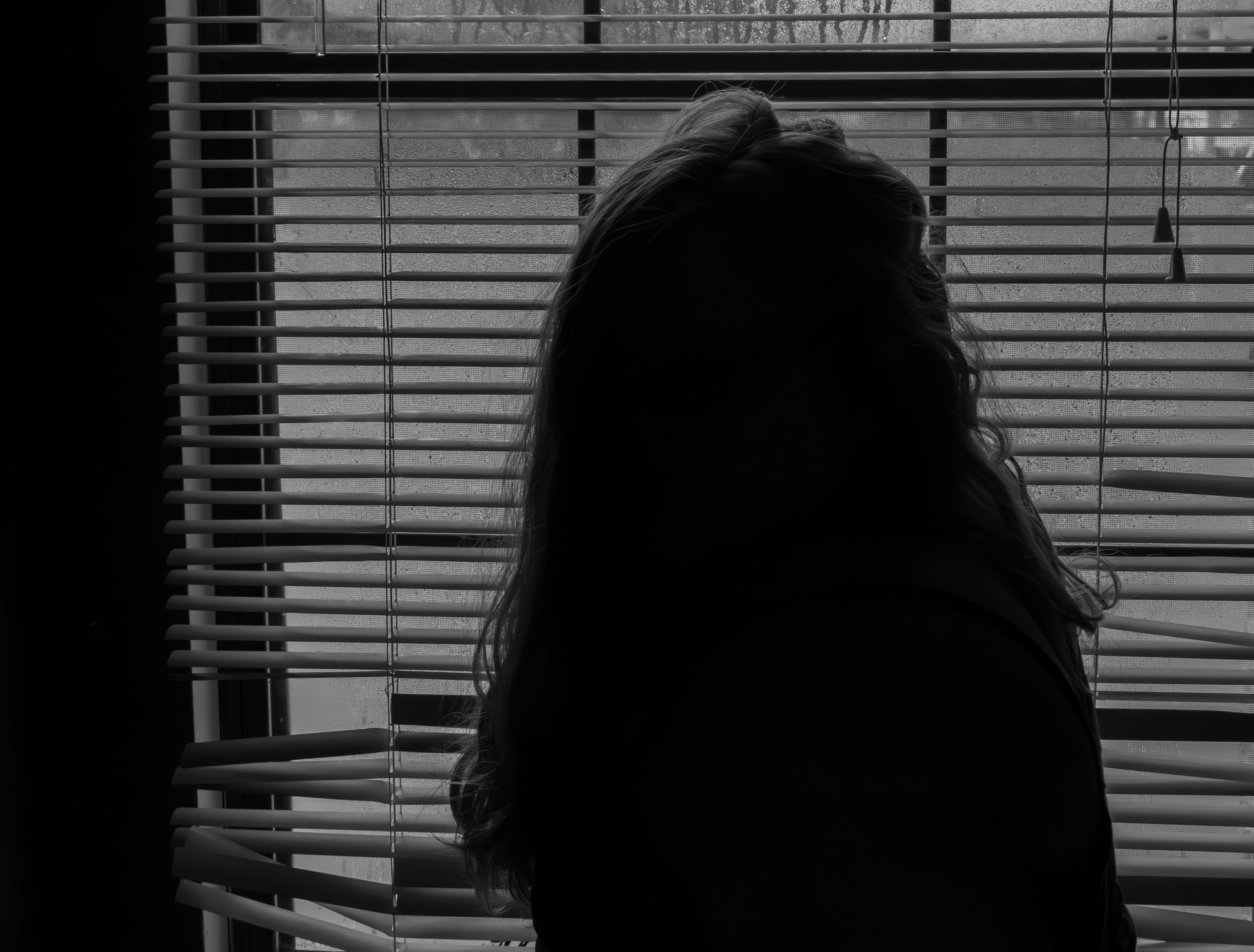 Silhouette of a figure against a backdrop of window blinds, creating a mysterious atmosphere.