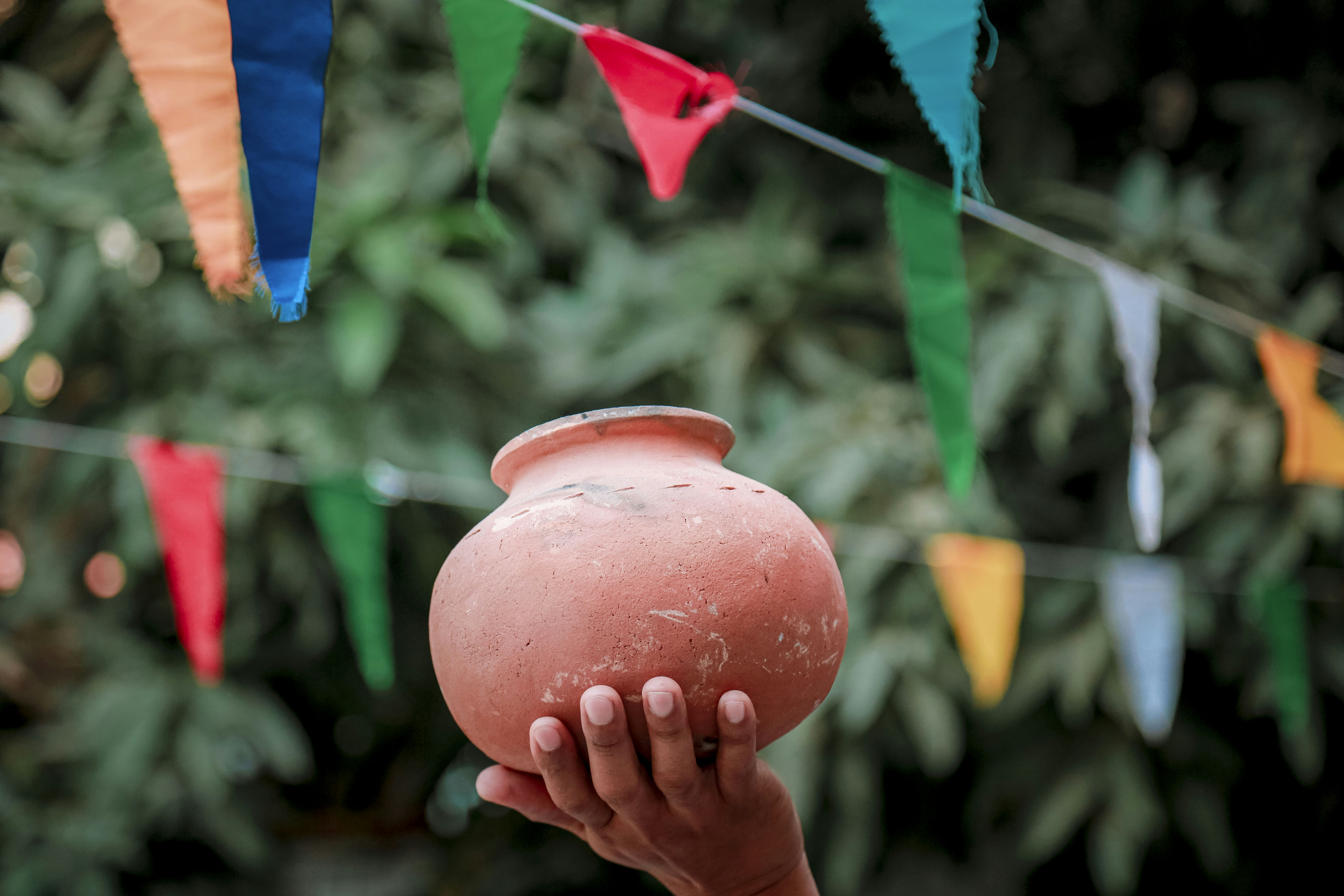 Earthy Vessel: A Hand Lifts a Clay Pot Against a Festive Backdrop
