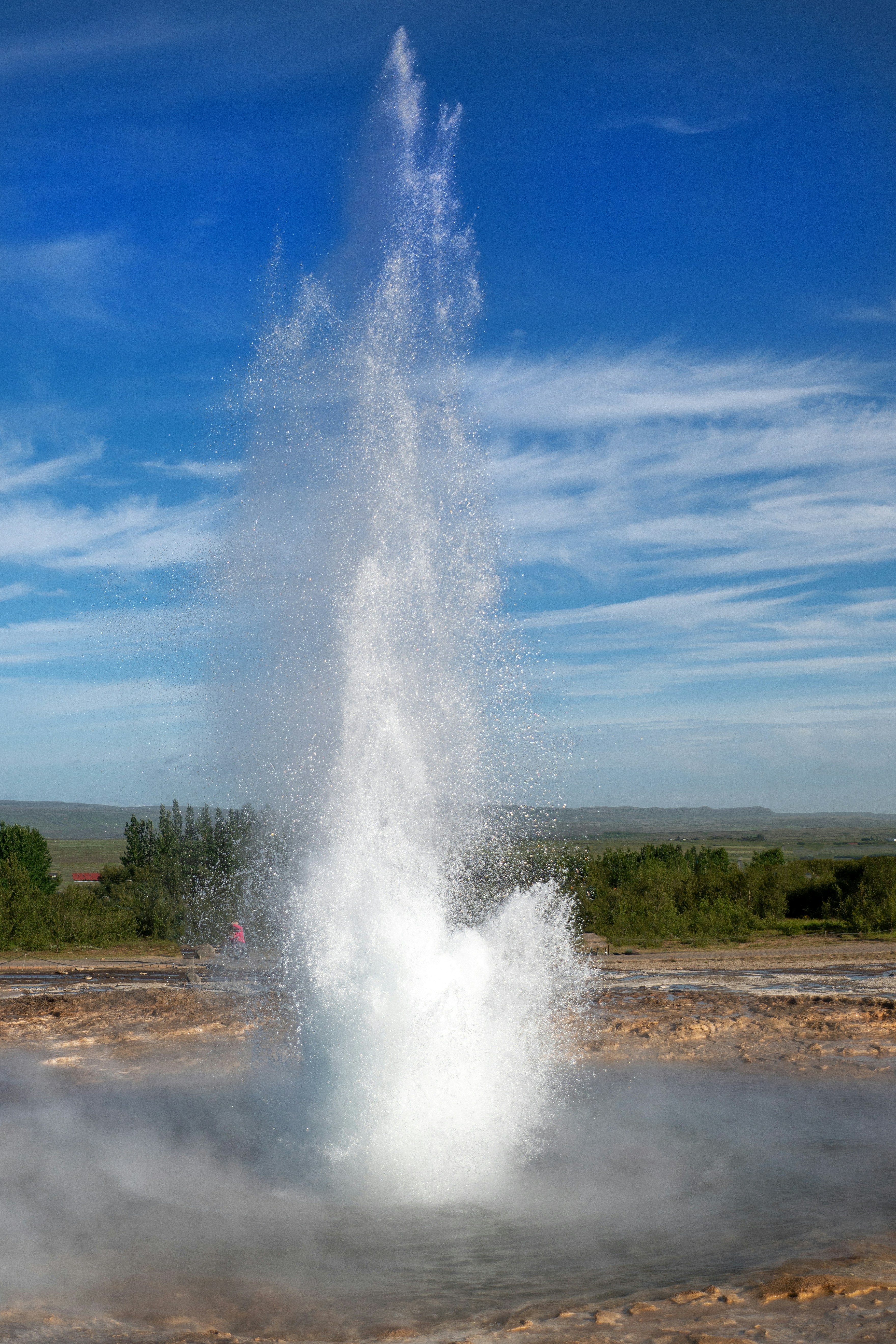 Geyser erupts from a barren plain, sending a tall plume into a crisp blue sky.