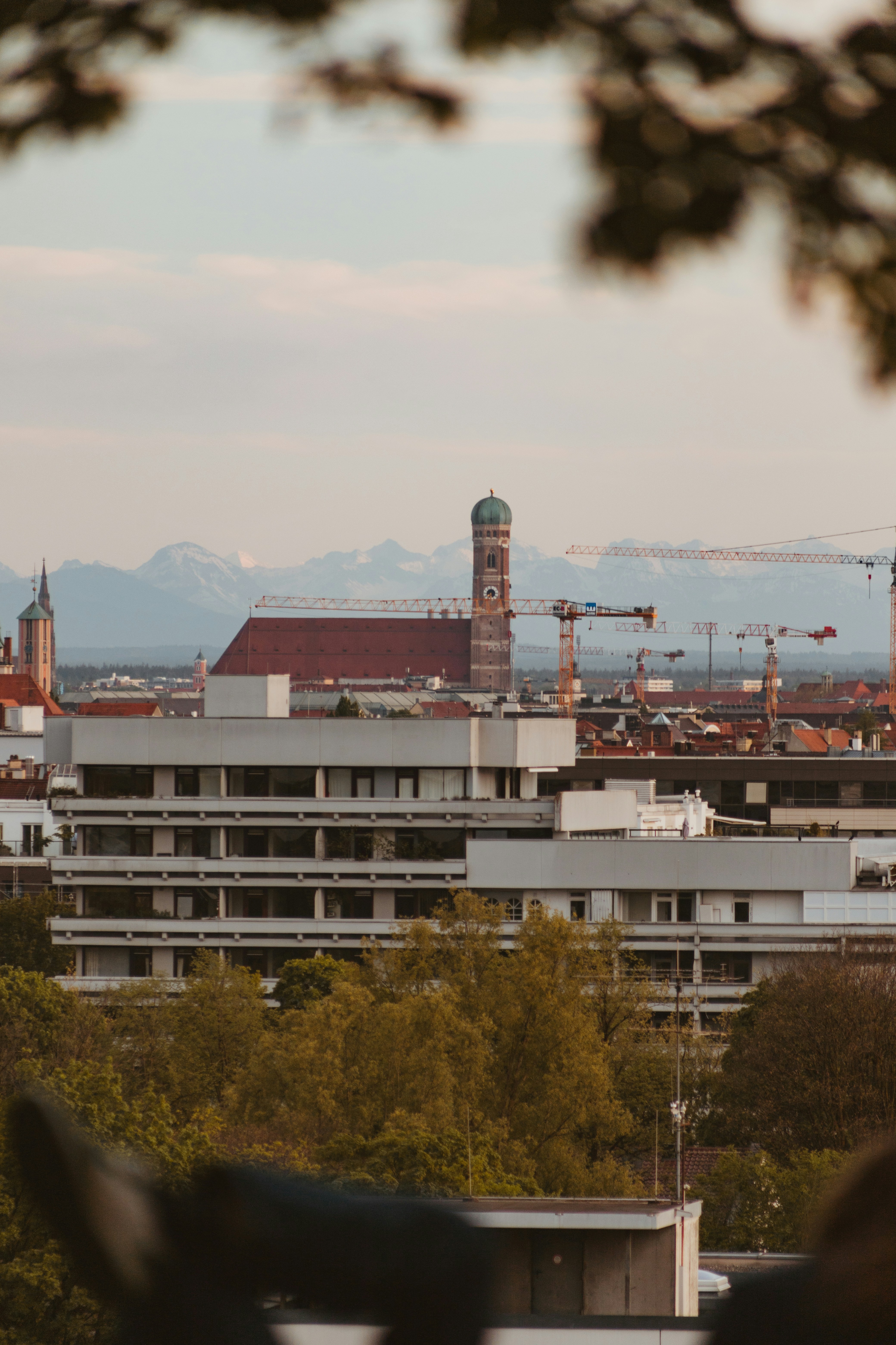Green-domed Clocktower Anchors a Crane-filled Cityscape Against an Alpine Horizon