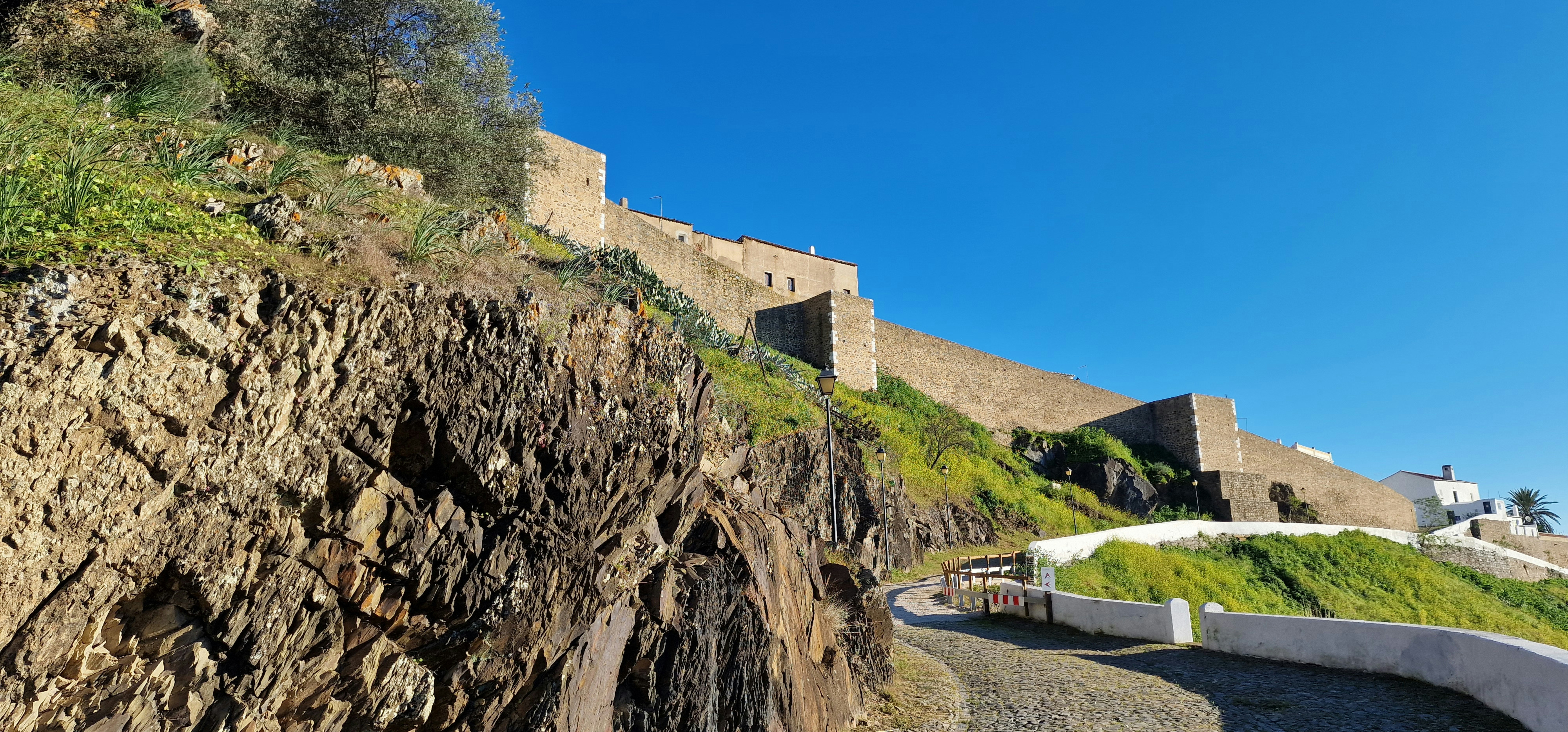 Rugged coastal ramparts meet sunlit promenade along a white-walled fortress
