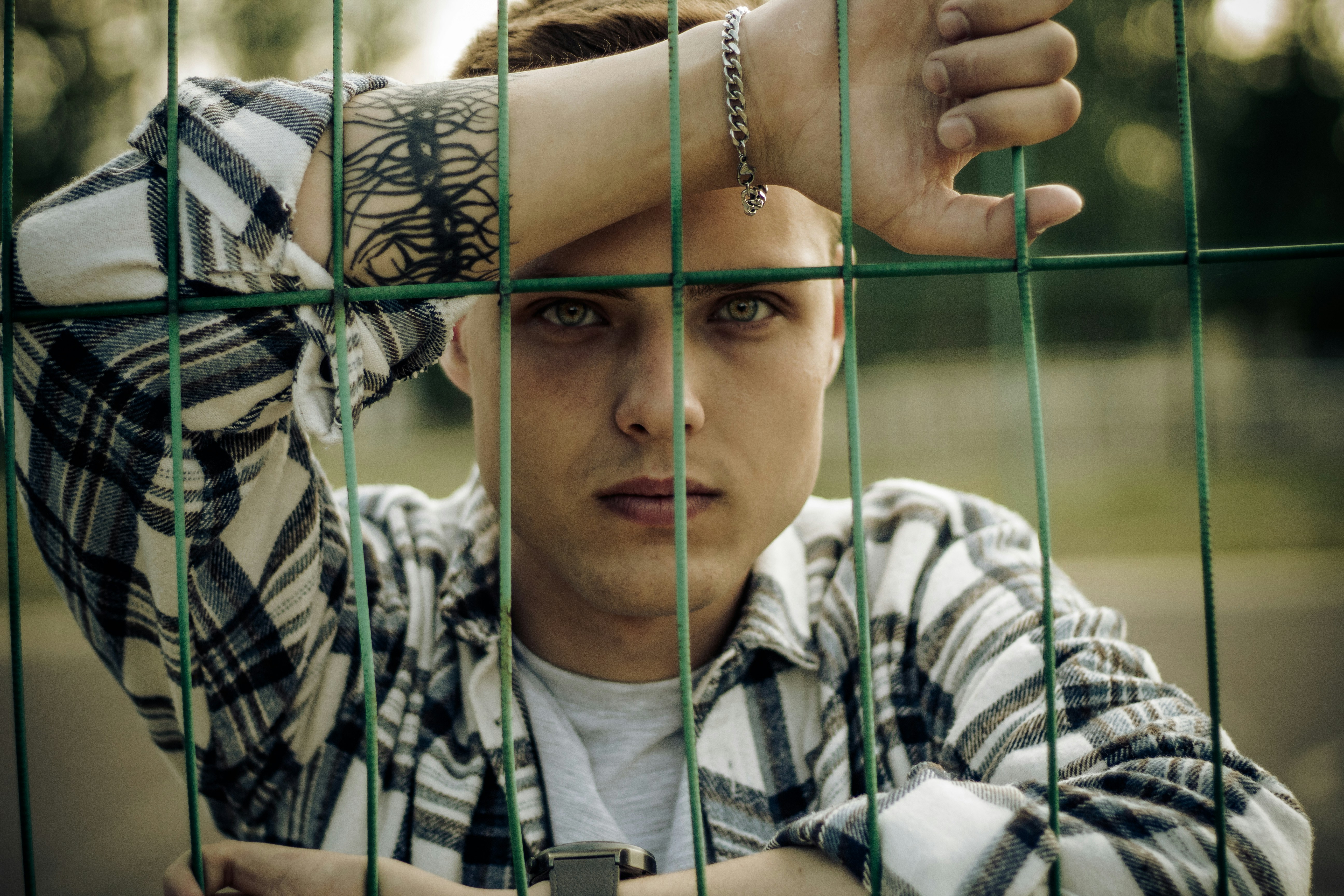 Person gazing through a wire fence with an arm resting on their head, wearing a plaid shirt.
