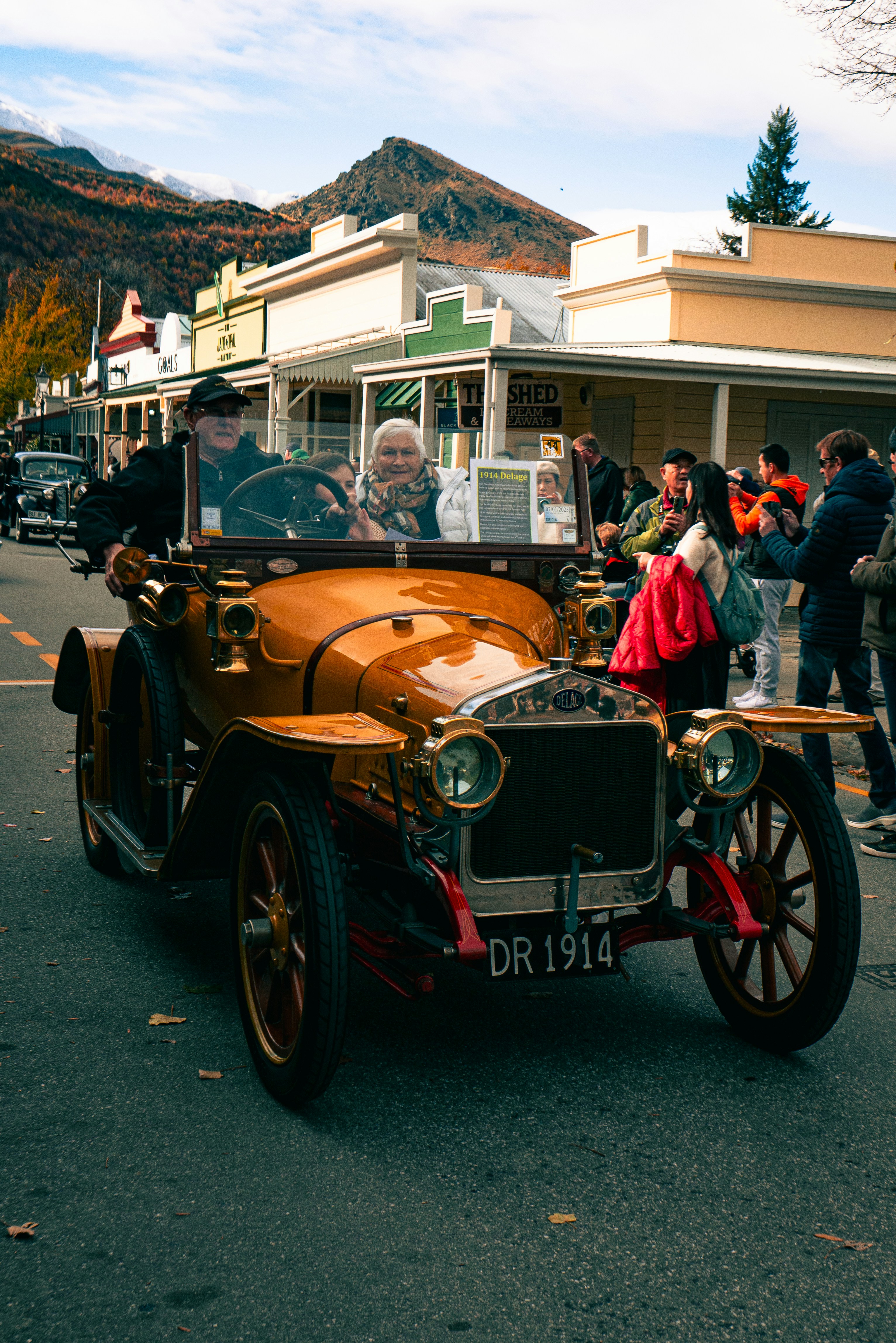 Gilded roadster threads gold through a mountain-town parade along pastel storefronts