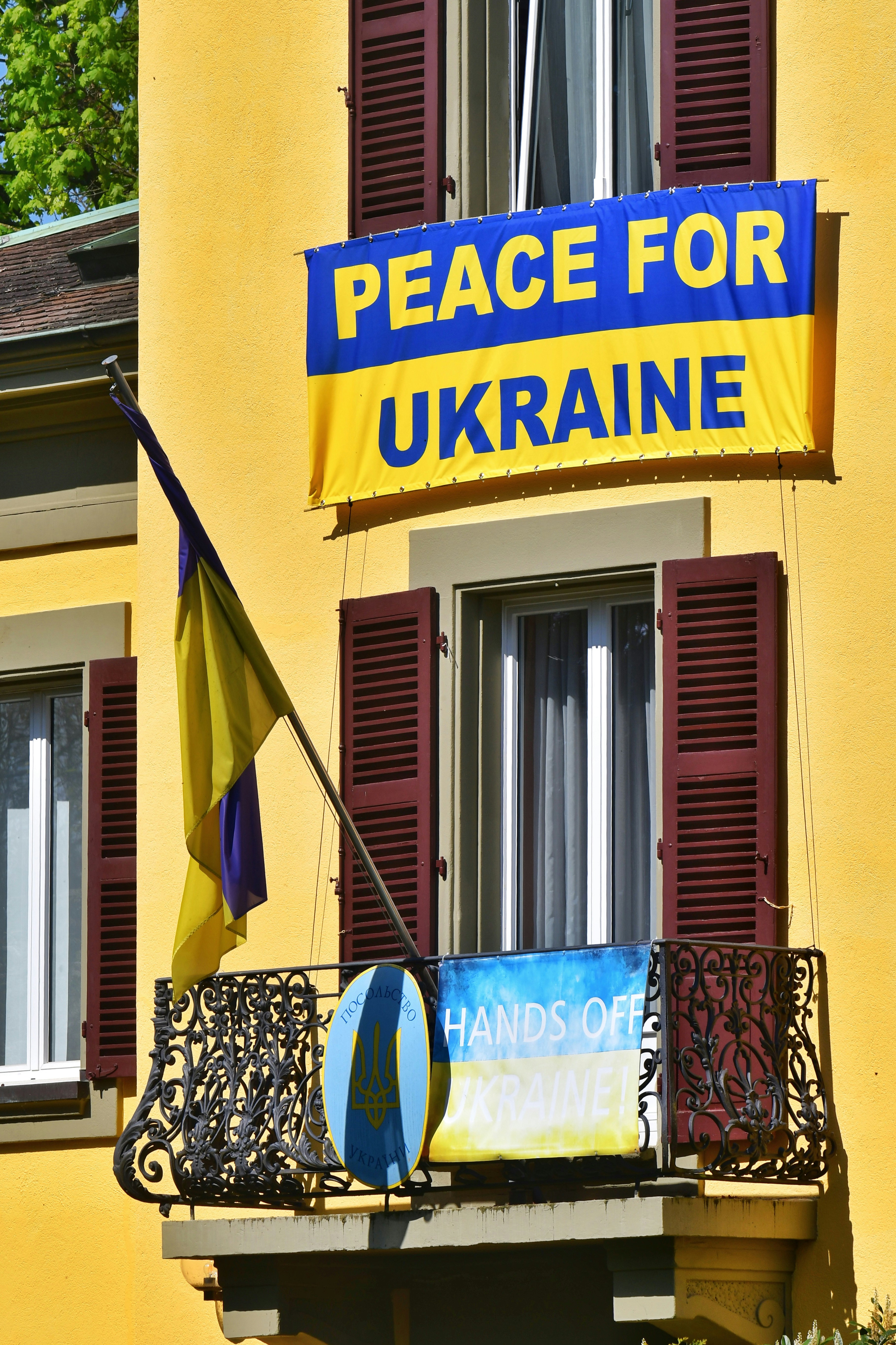Sunlit Yellow Facade: Peace for Ukraine Above a Wrought-Iron Balcony