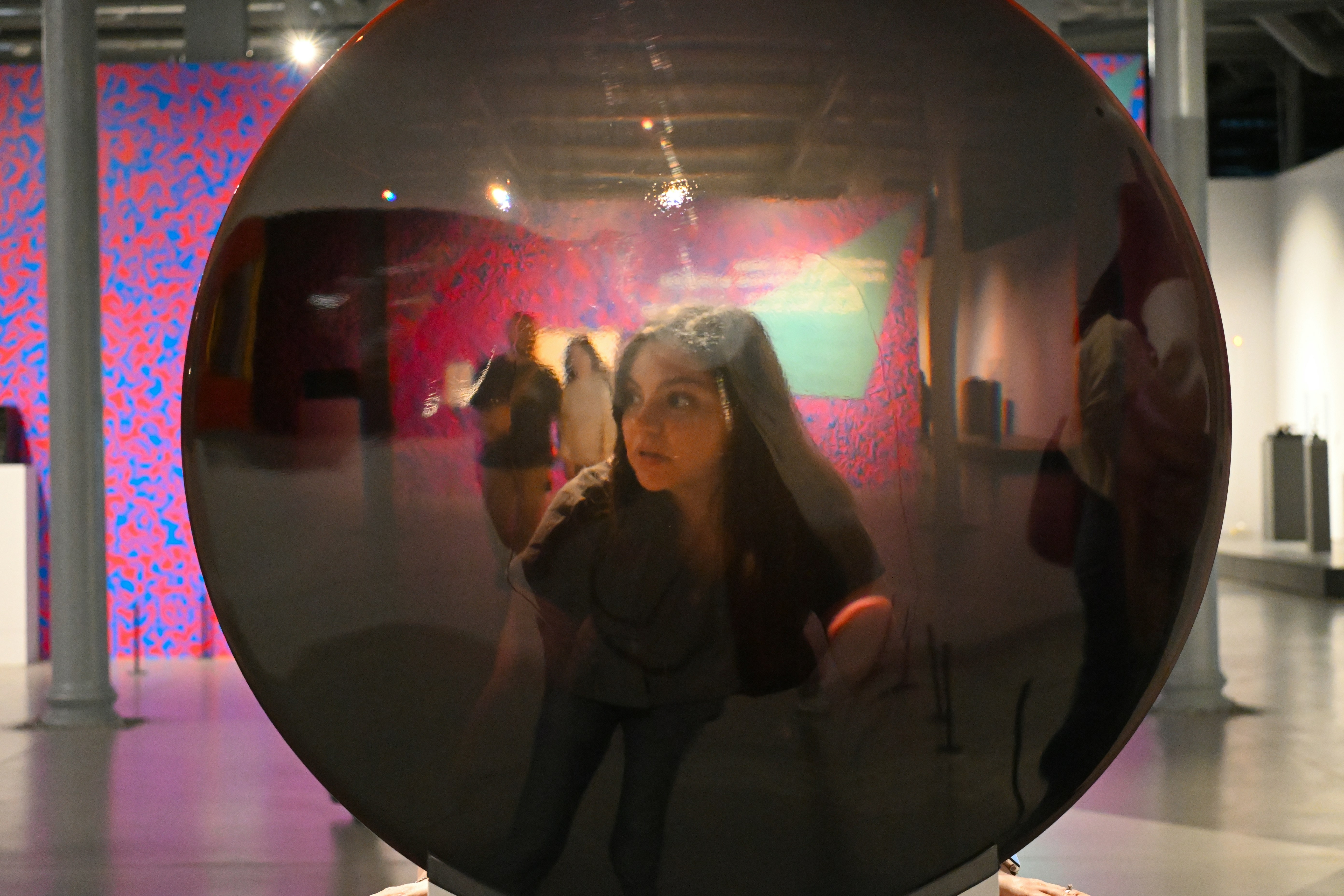 Reflected Portrait in a Crimson Sphere: A Glimpse of People and Pattern in a Modern Gallery