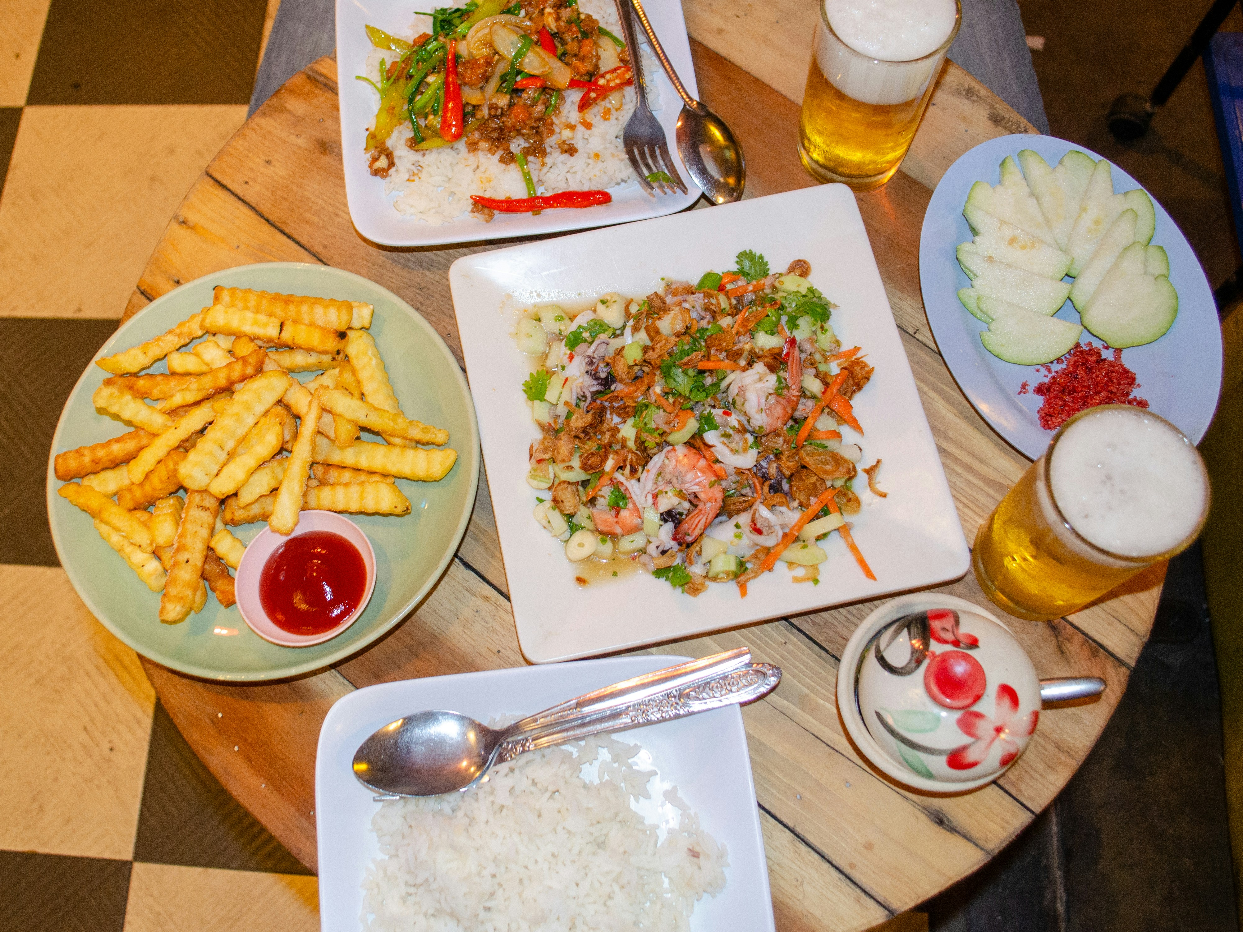 Assorted dishes with fries, rice, and vegetables on a round table with drinks.