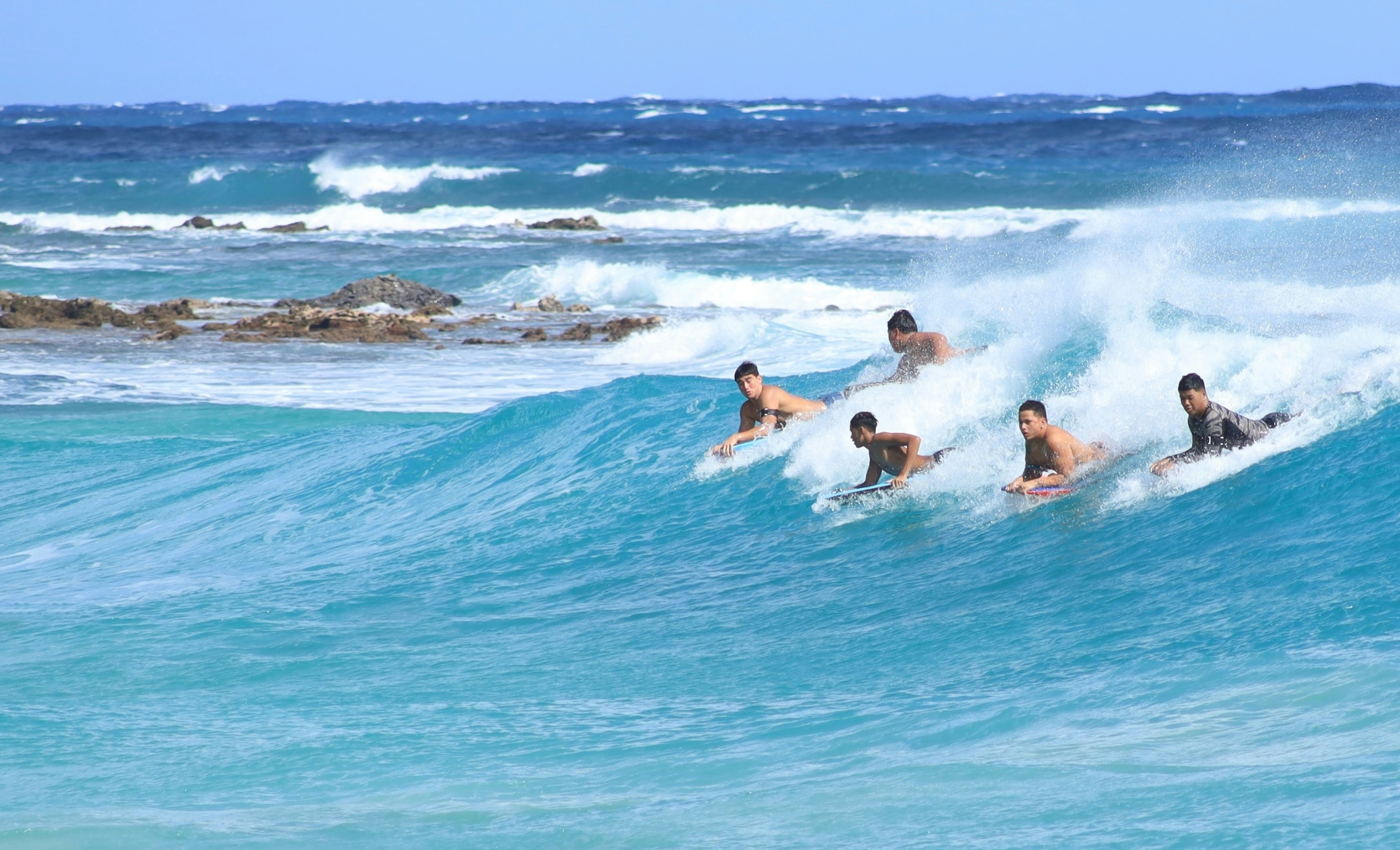 Surfers expertly navigating a curling wave in clear blue ocean waters.