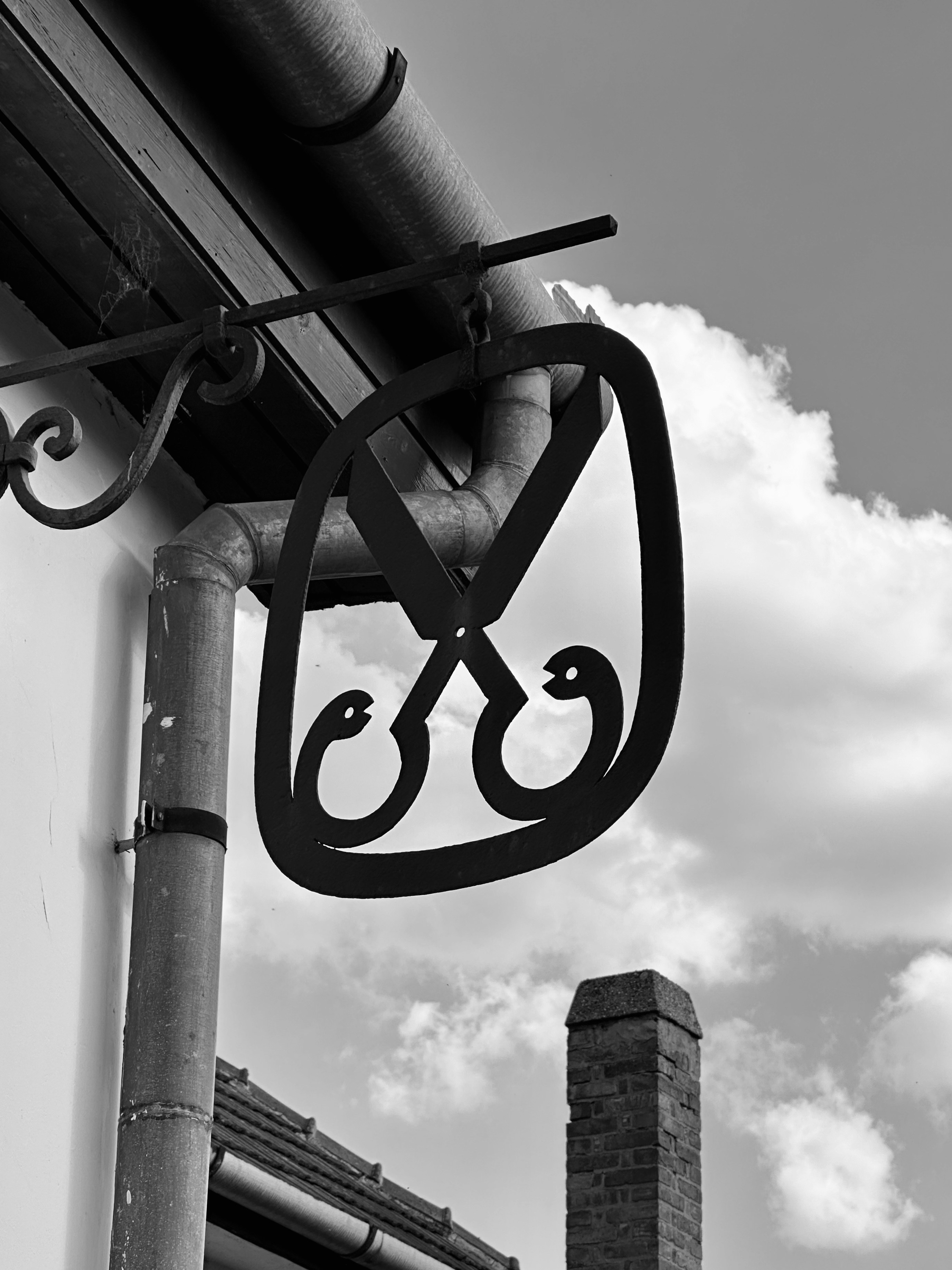 Twin Bird Silhouettes on a Curved Iron Sign Against a Cloudy Sky