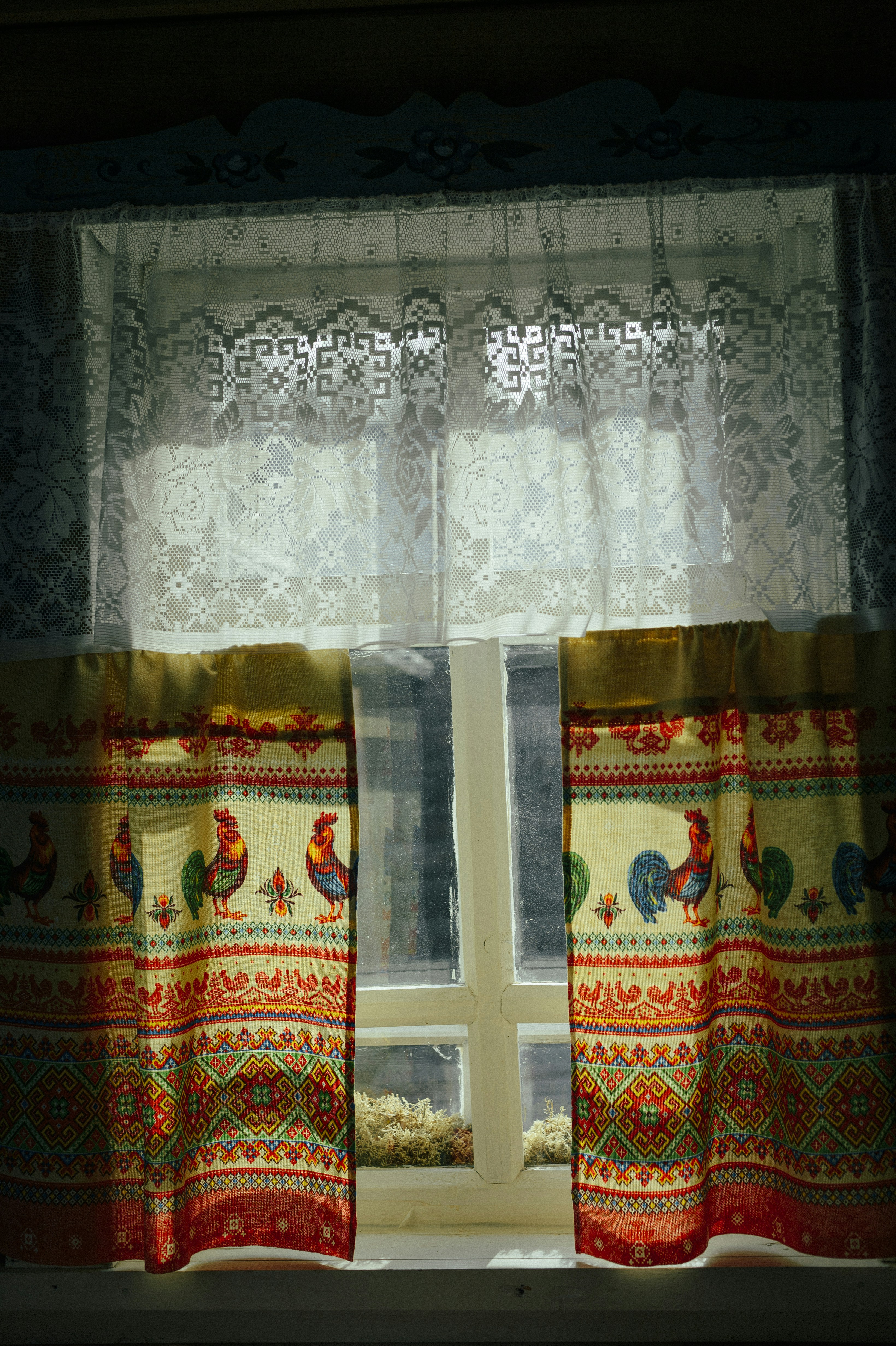 Sunlit Window Nestled Between Lace and Rooster-Patterned Curtains