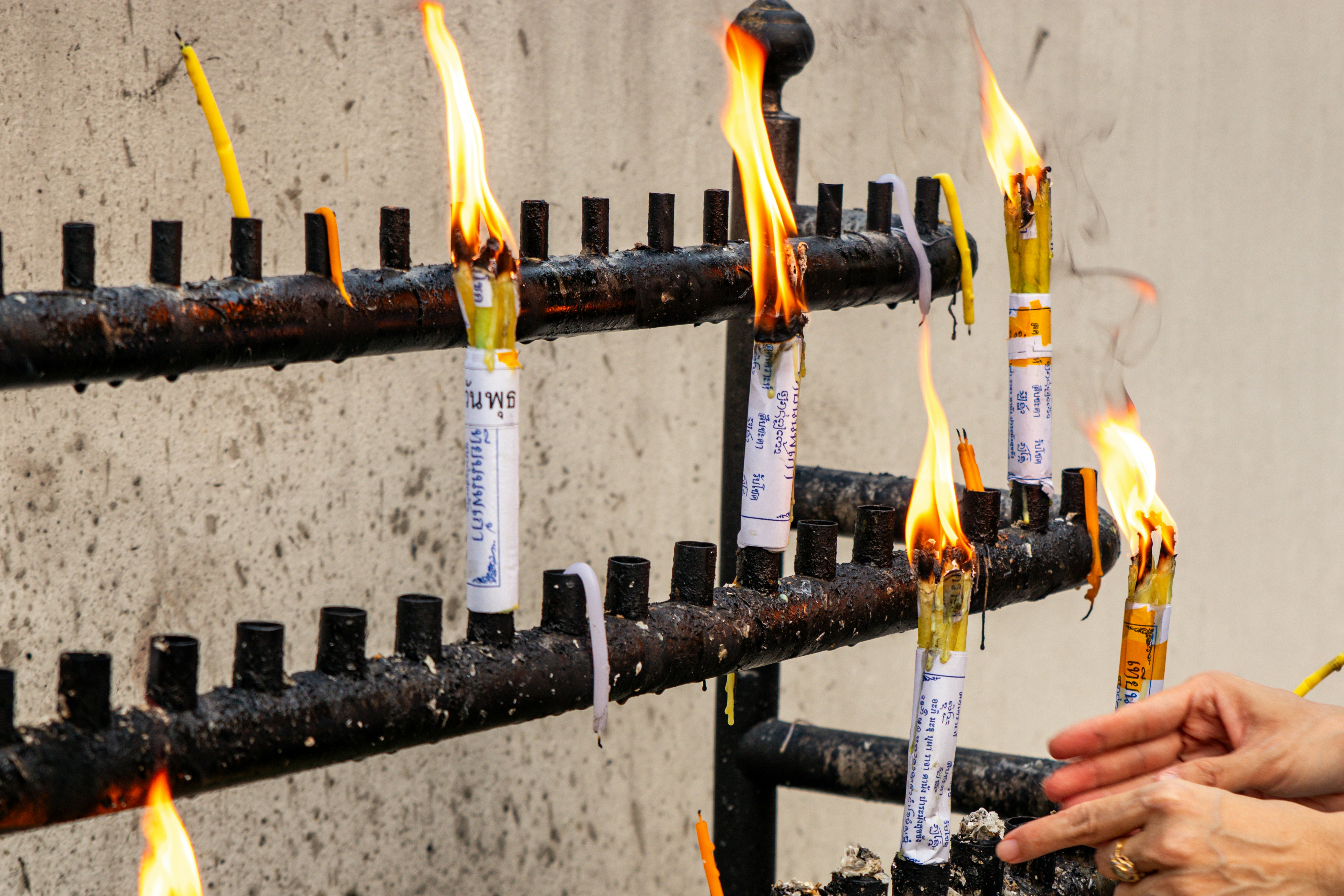 Candles burning on a metal stand at a Buddhist temple, with hands adjusting them.