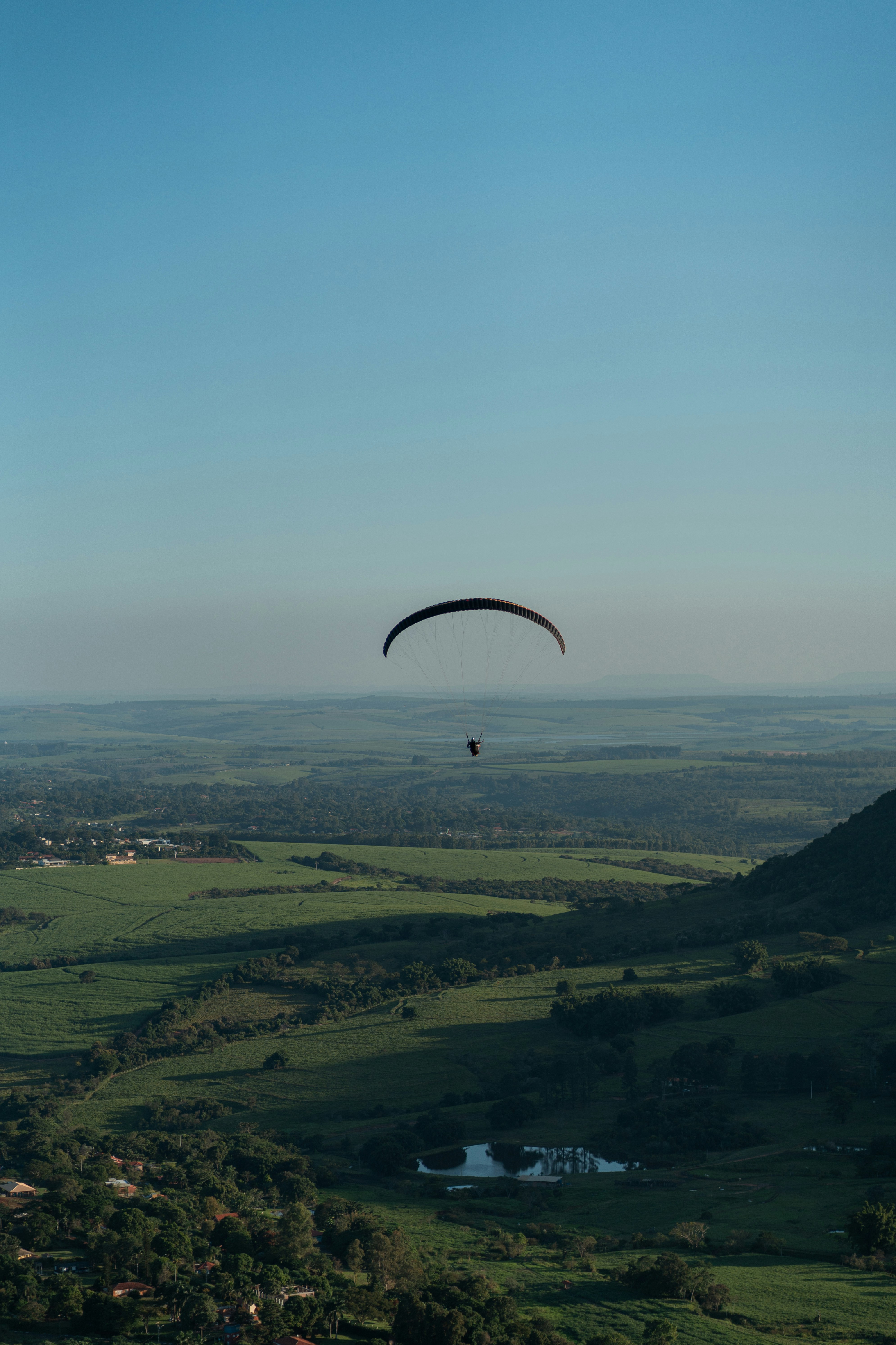 Suspended Arc: A Paraglider Drifts Above the Rolling Countryside