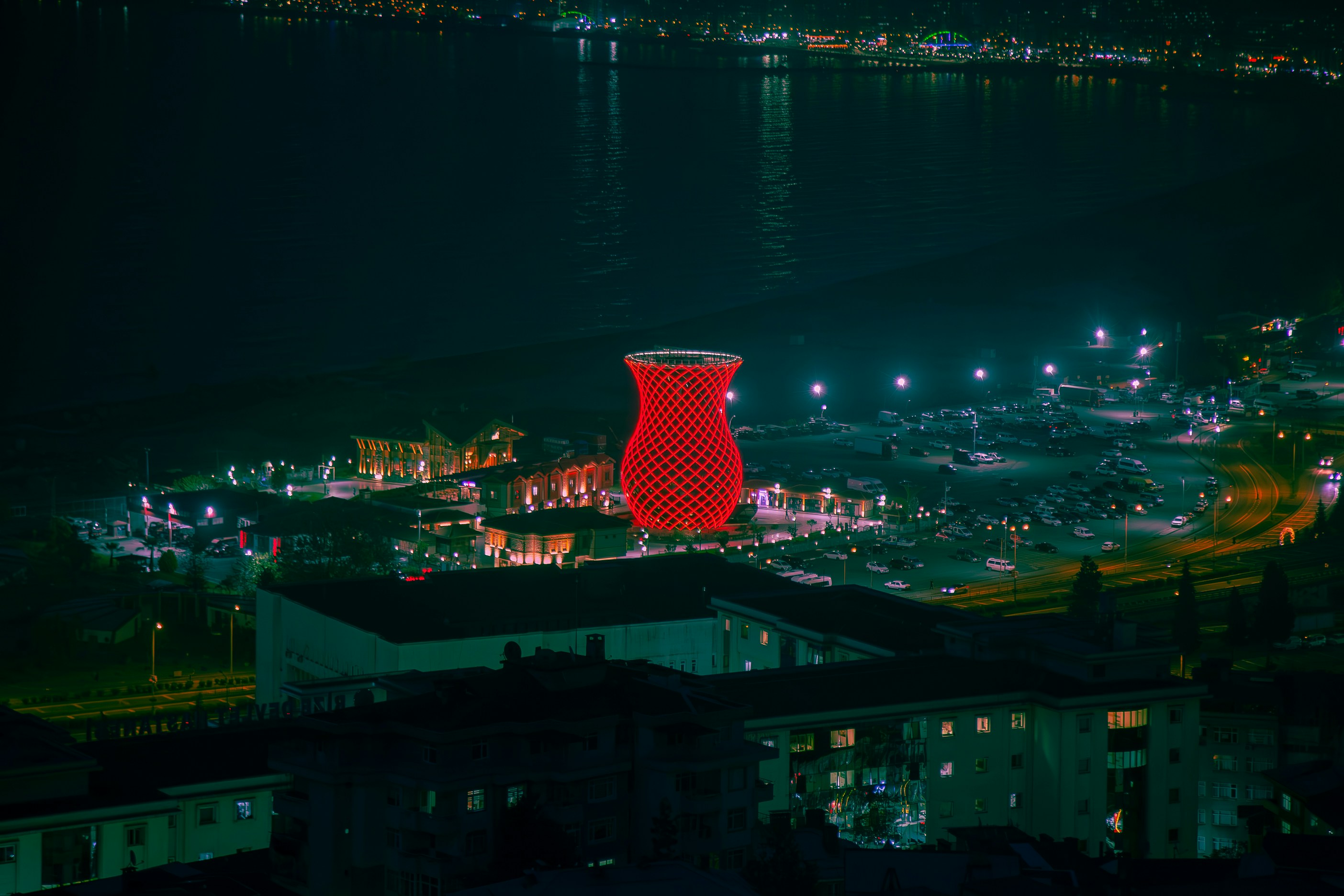 Brightly lit tea glass-shaped tower glowing at night in Rize, Turkey, surrounded by city lights.