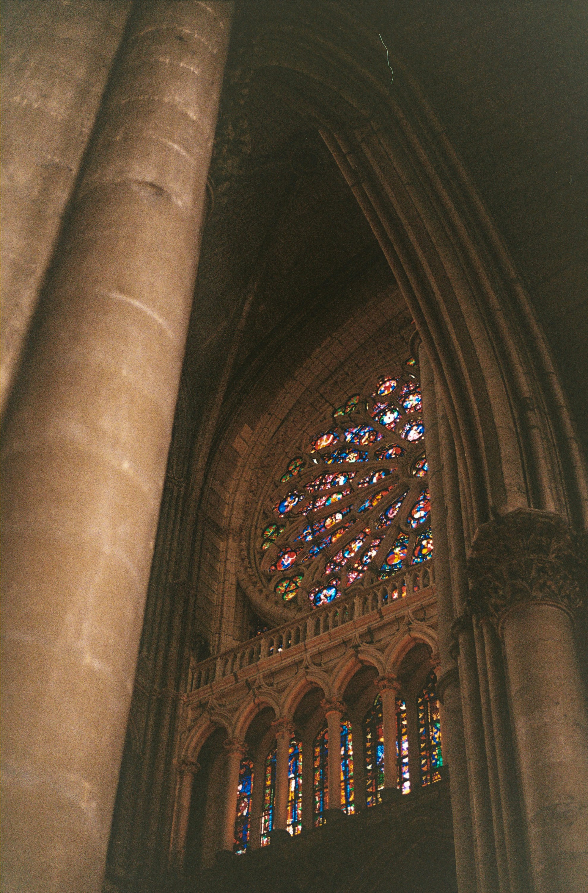 Photograph of a Gothic cathedral interior featuring a circular rose window framed by towering arches and worn columns, bathed in warm amber light.