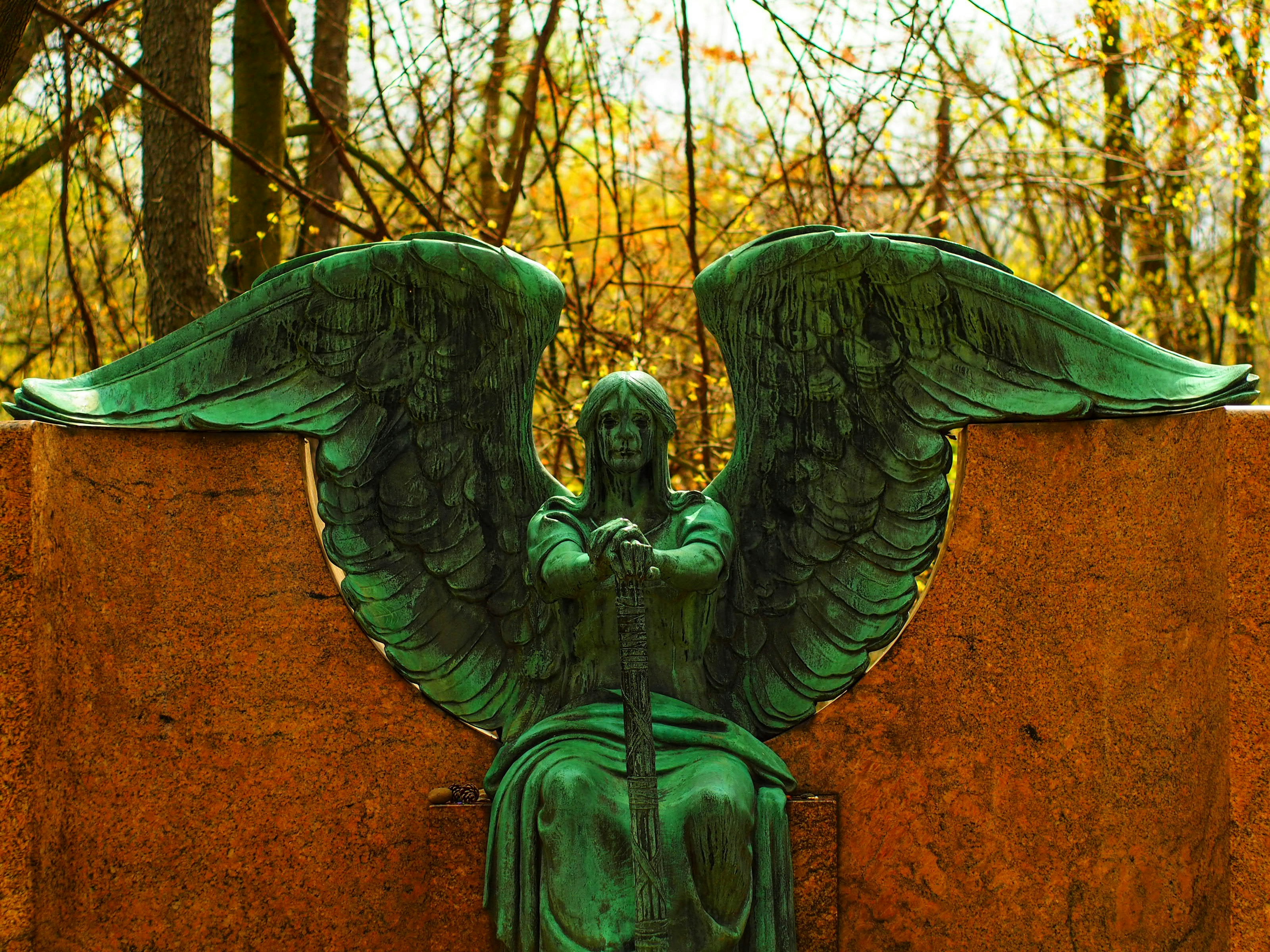 A statue of an angel sitting on top of a stone wall photo – Free ...