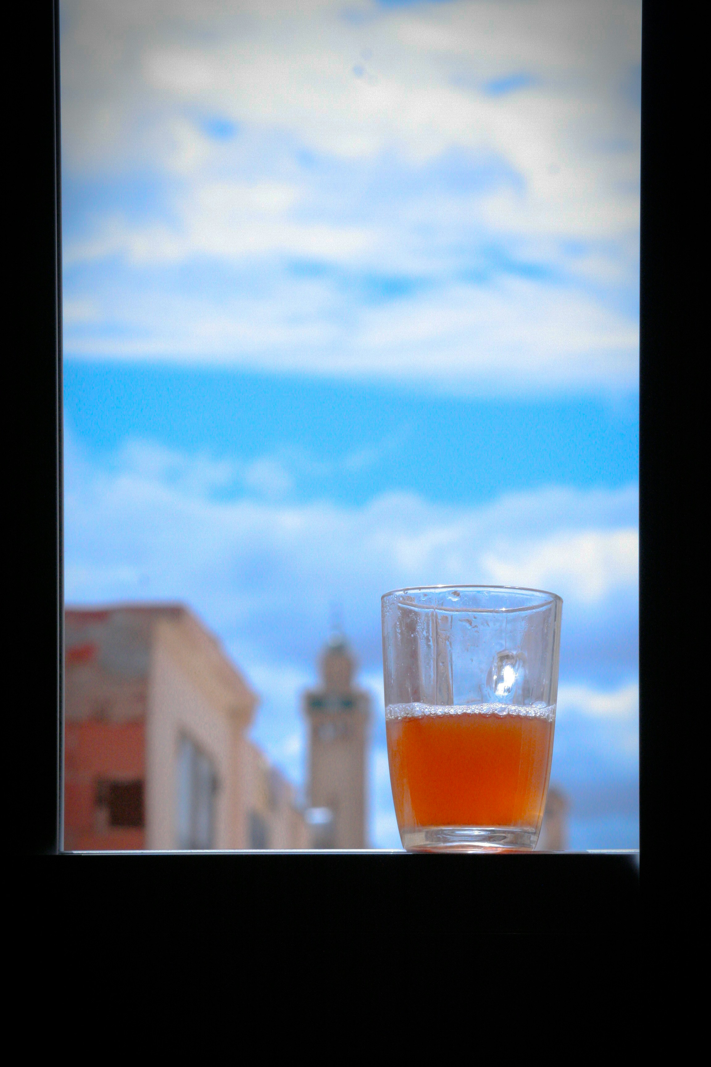 Orange Glass on a Window Sill Framed by Sky-Blue Cityscape