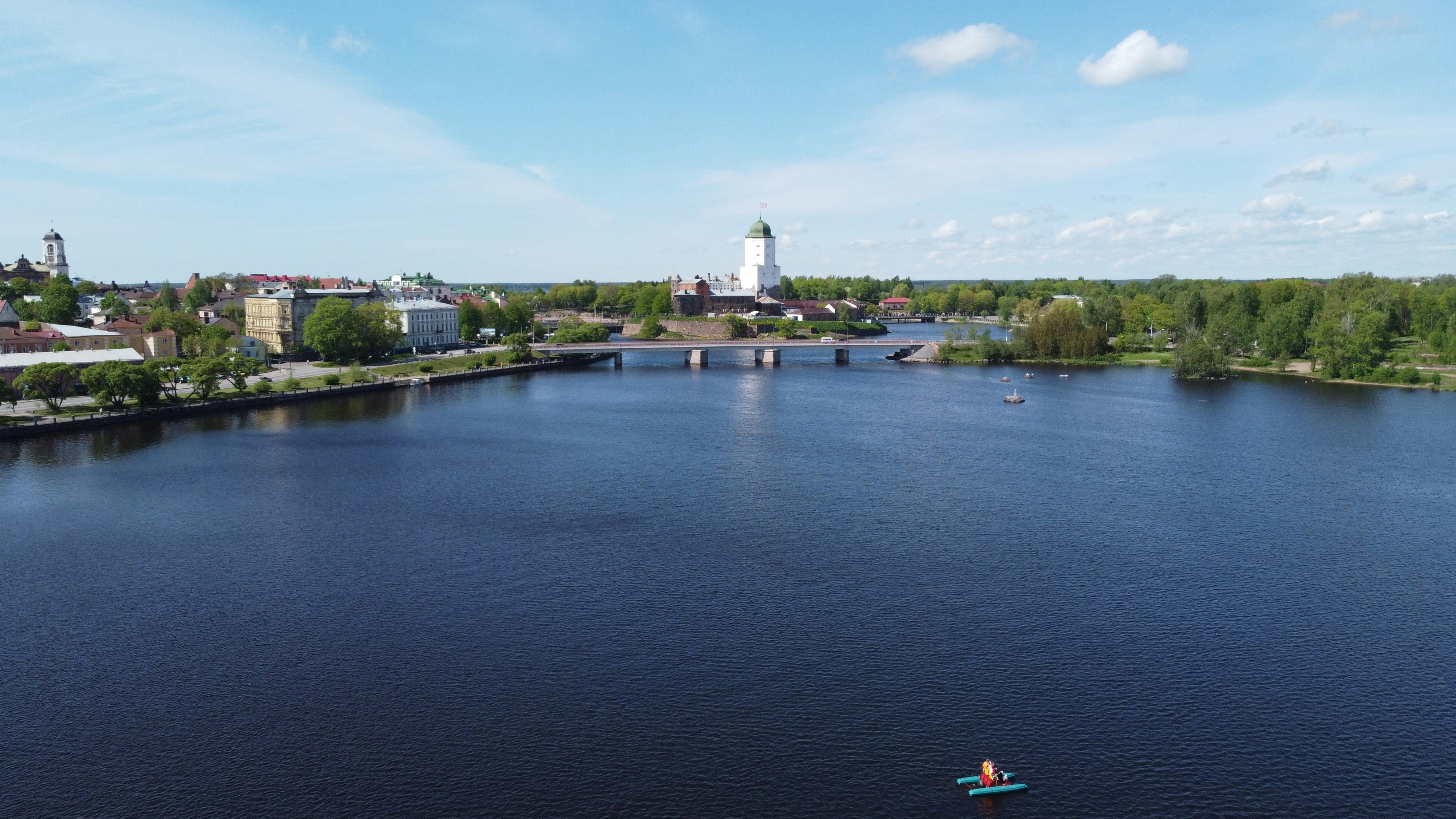 Kayaker paddling on a calm lake under a clear blue sky with a distant view of a white lighthouse.