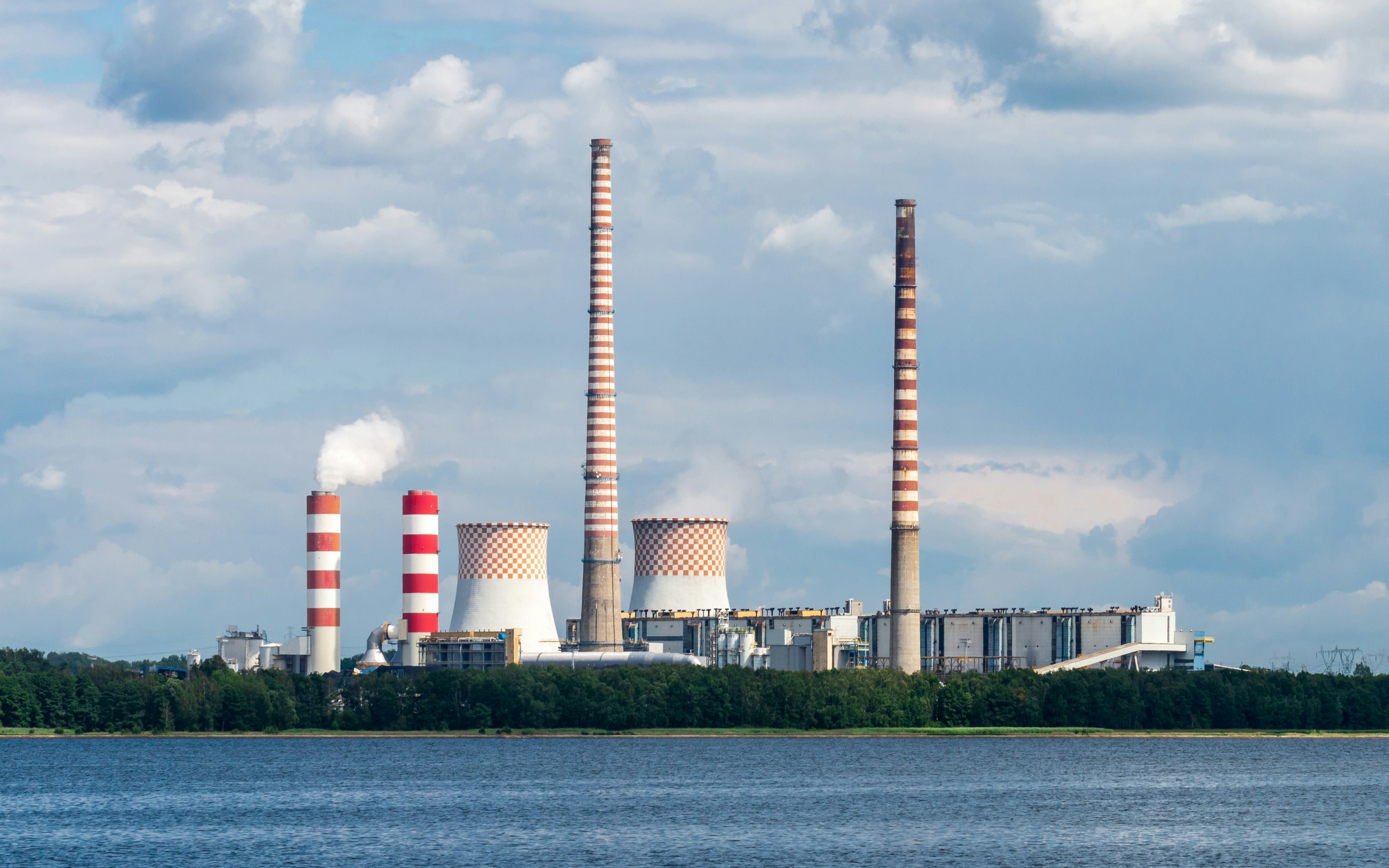Smoke stacks rise from a factory near a body of water photo – Free ...