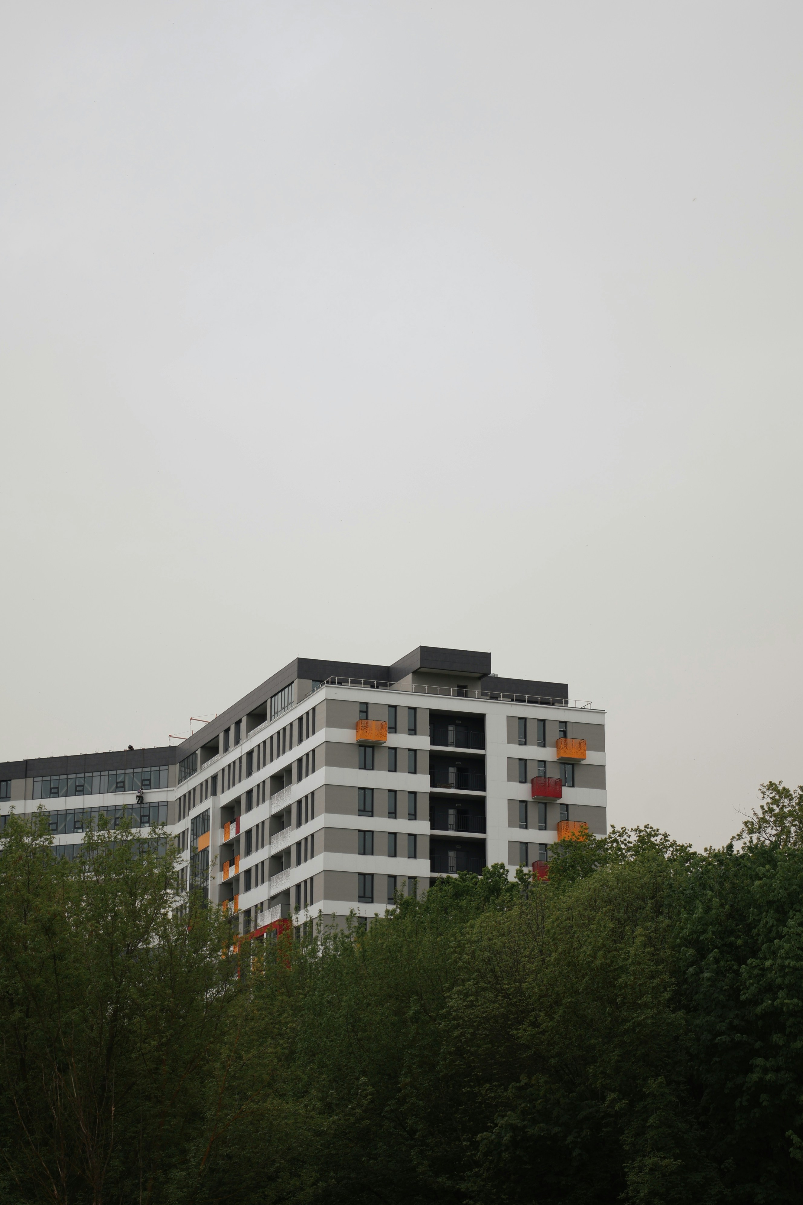 Orange-Accented Block Rising Through Green: Urban Minimalism Under Gray Skies