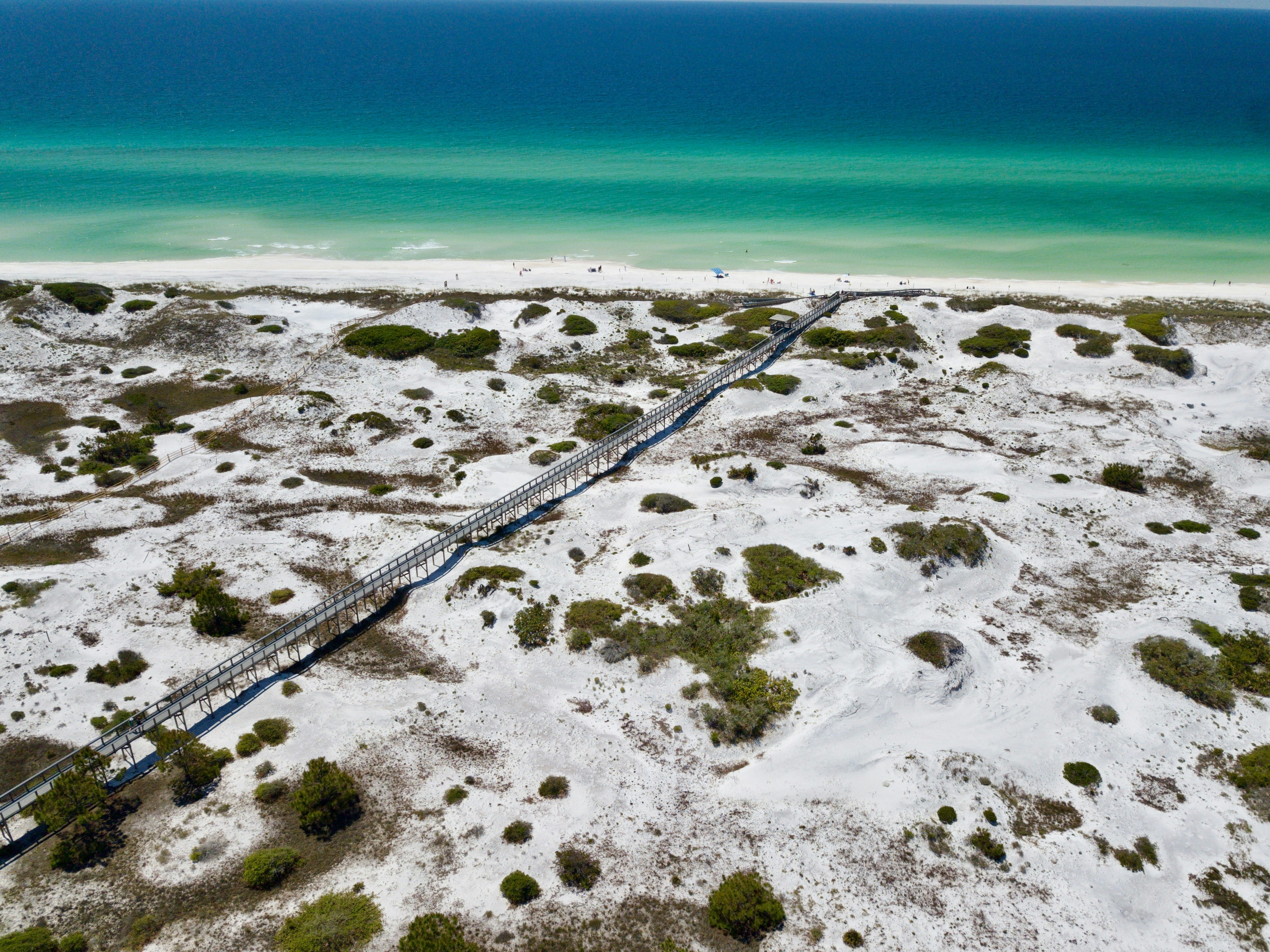 Aerial view of a boardwalk stretching across white dunes towards a turquoise ocean.
